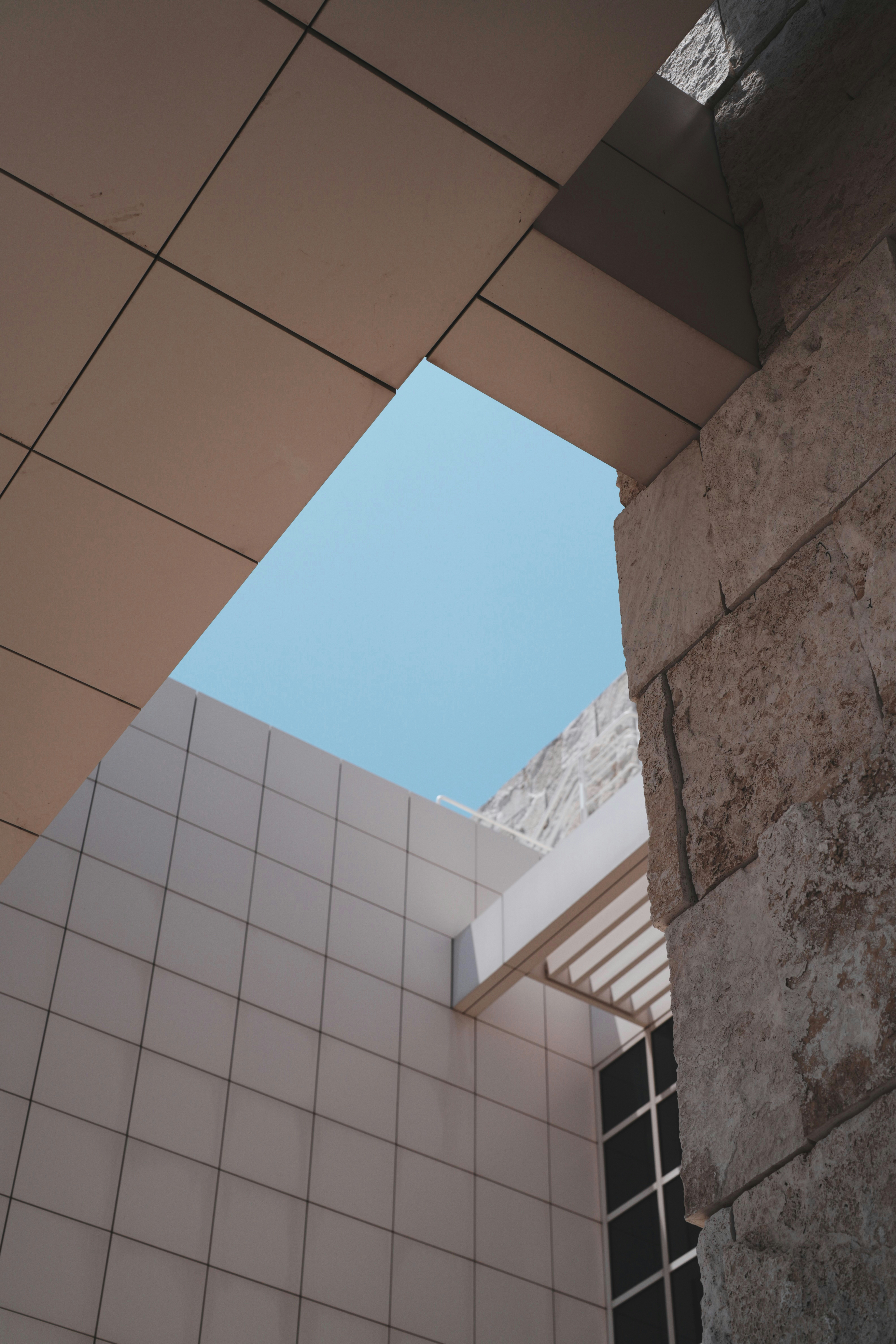 Concrete and tile architectural forms frame a sliver of blue sky, creating a geometric composition with strong diagonals and contrasting textures.