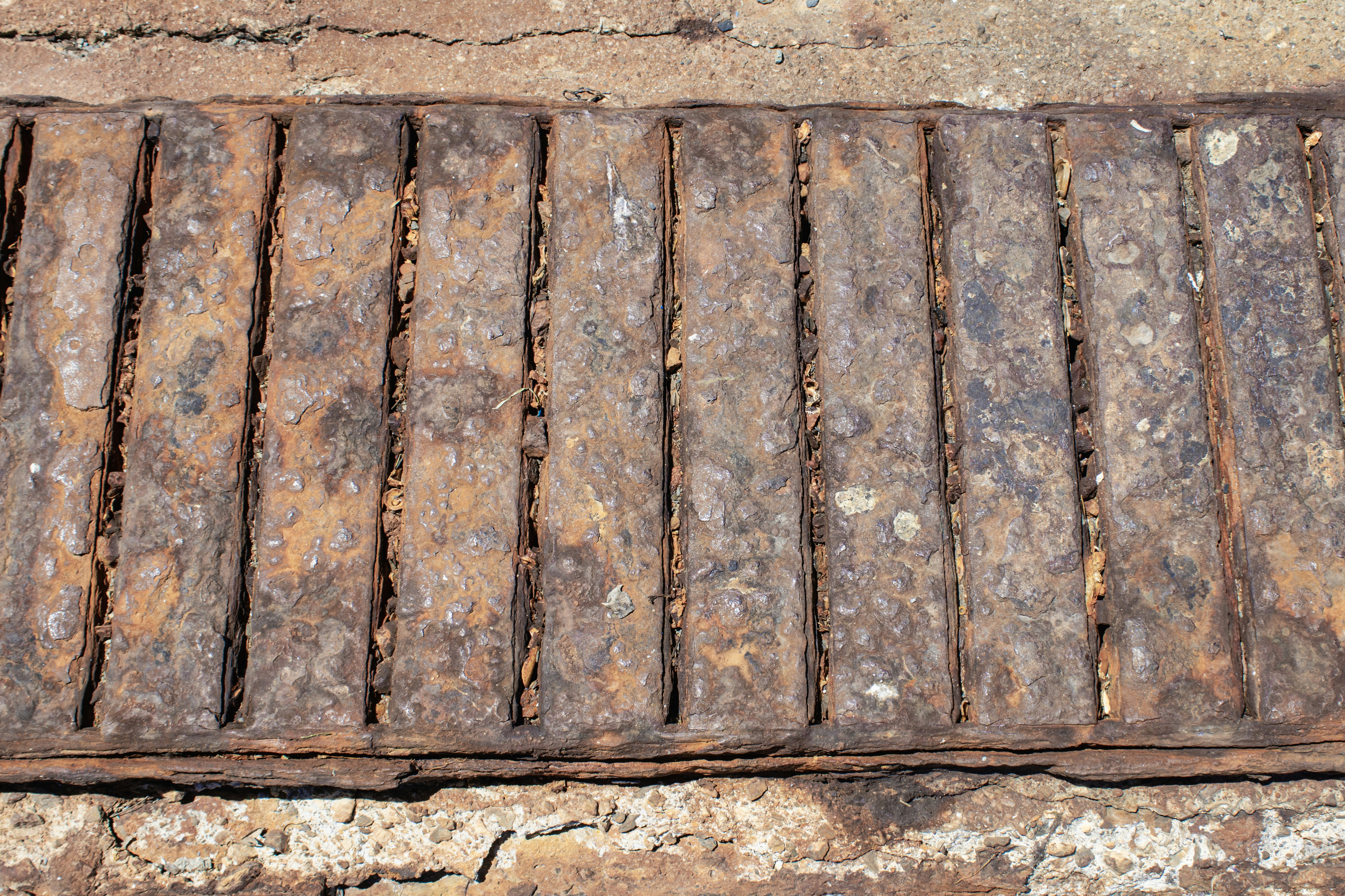 Rusted grate over concrete trench: weathered lines and patina in a linear pattern