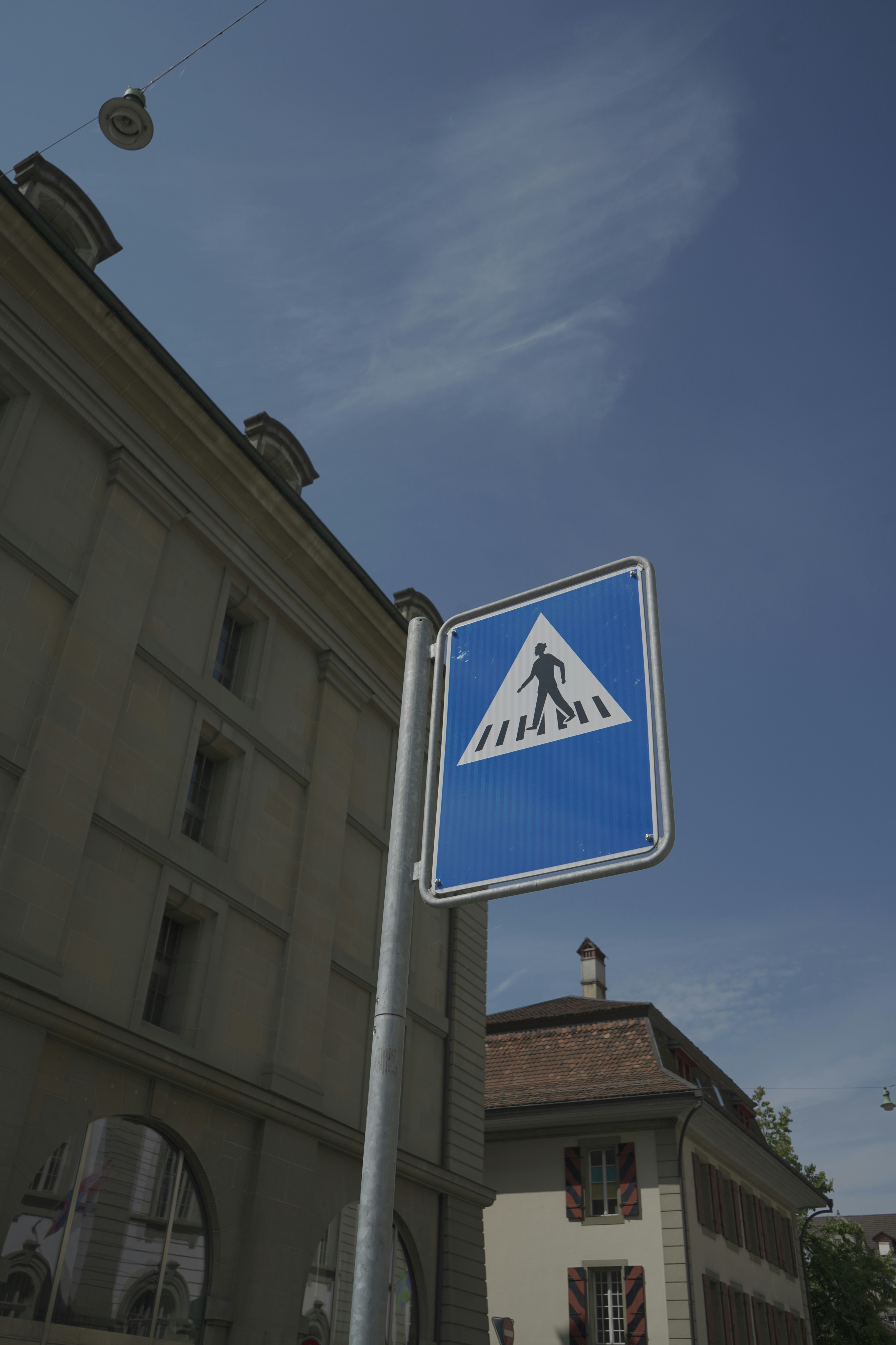 Blue Pedestrian Crossing Sign Reaches for Sky Above Historic Facade