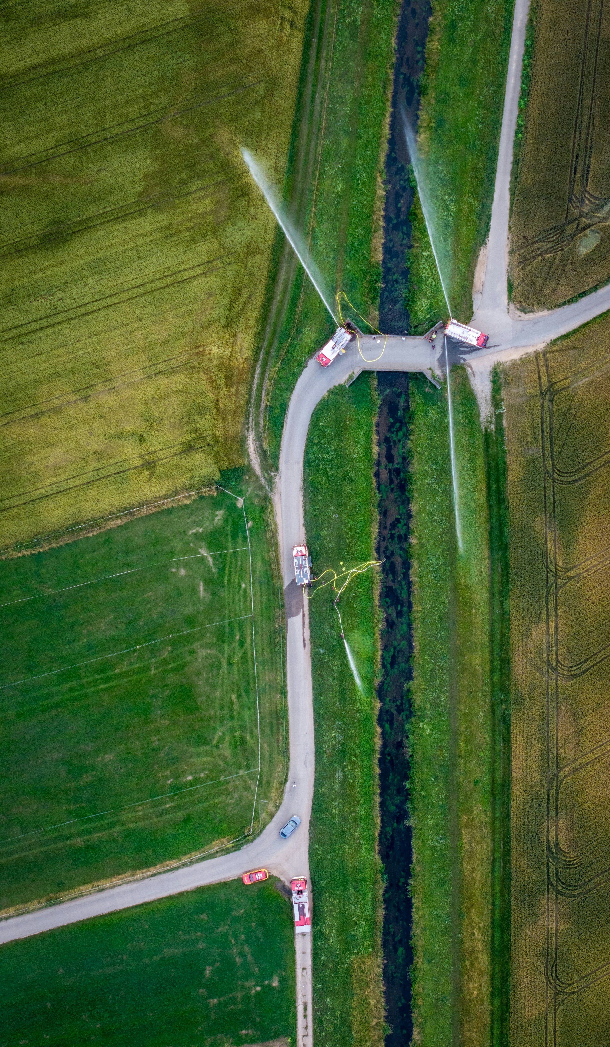 Fire trucks spray water across rural fields and a canal.