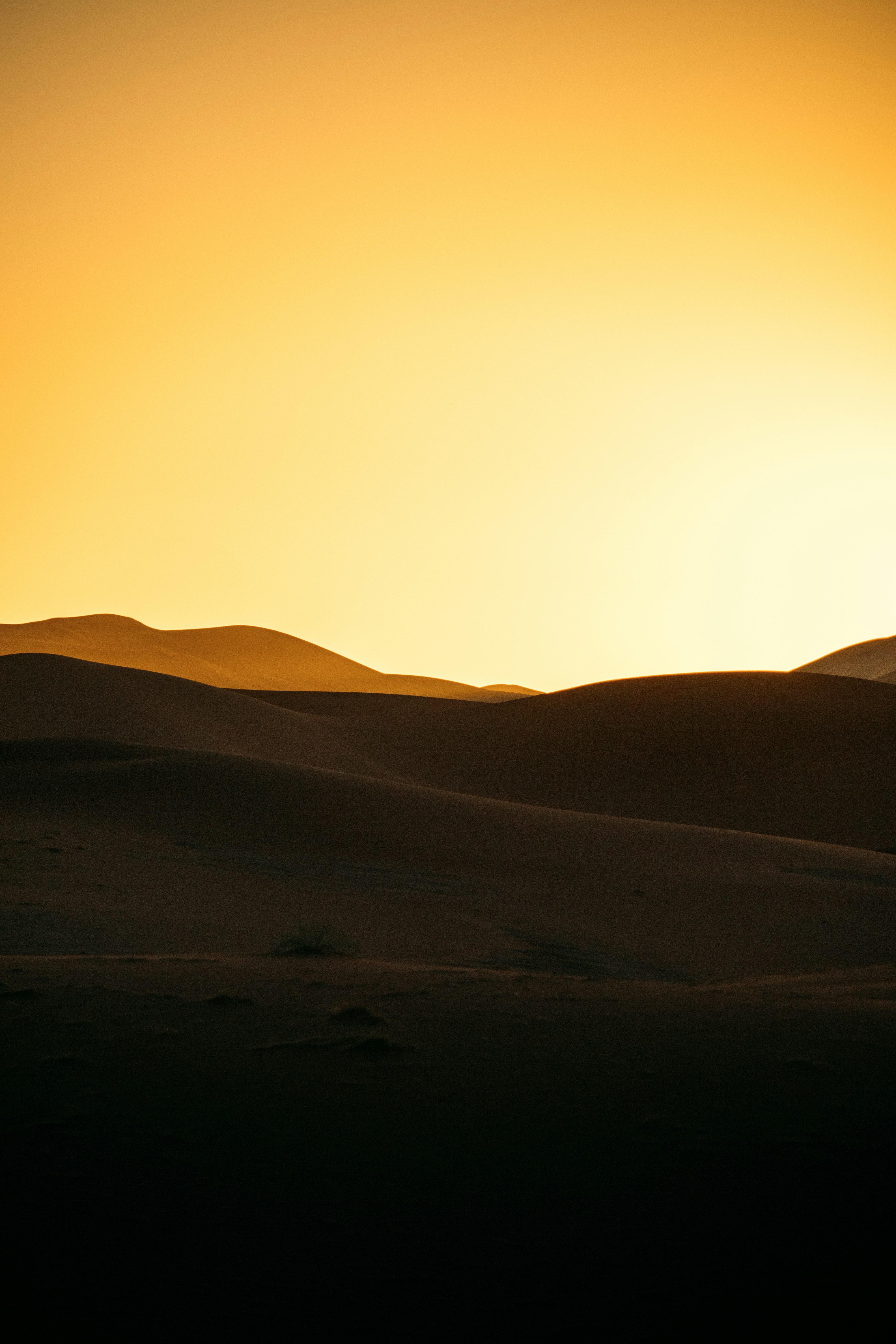 Dark sand dunes silhouetted against a vibrant orange sunset sky.