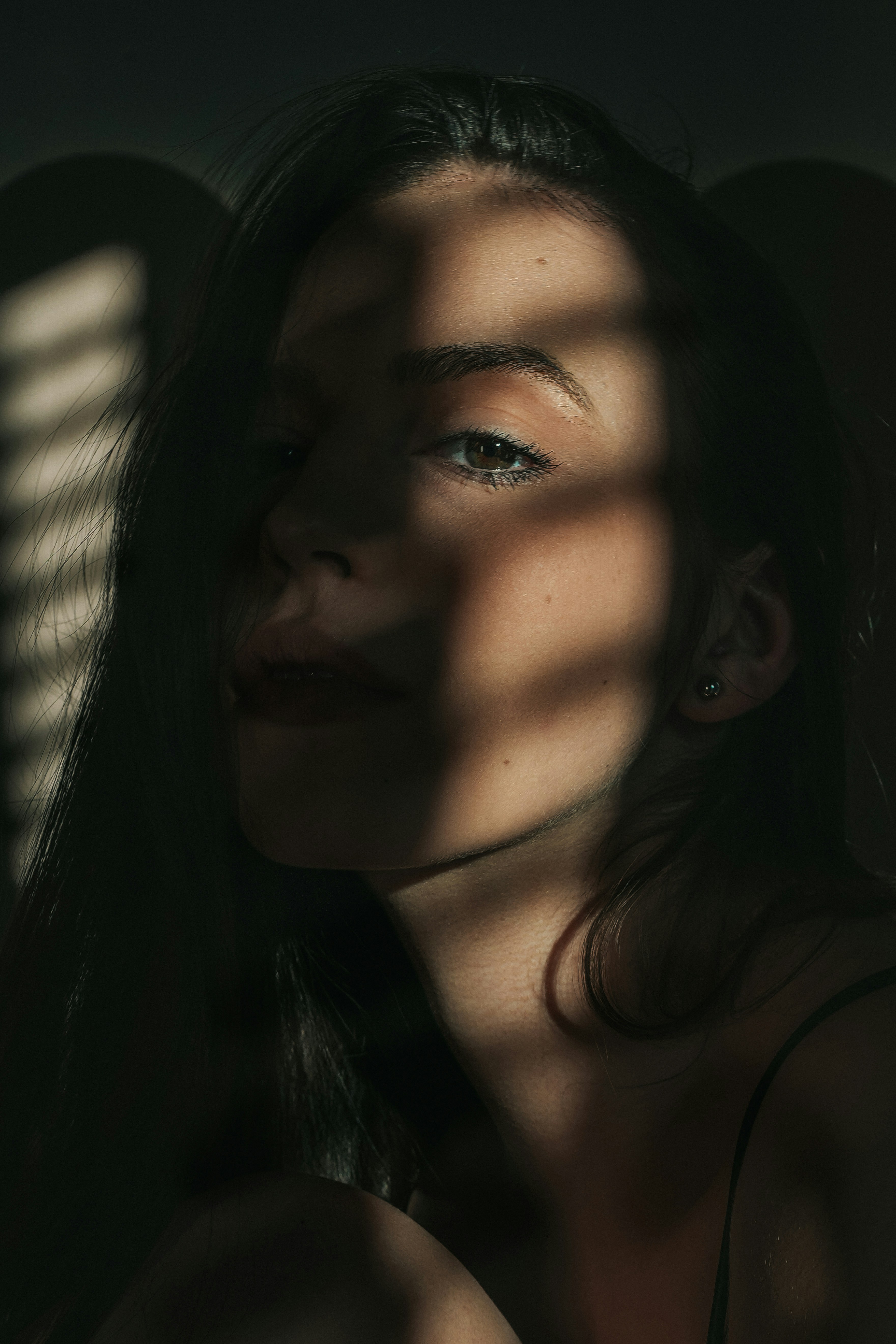A woman's face partially illuminated by sunlight through blinds.