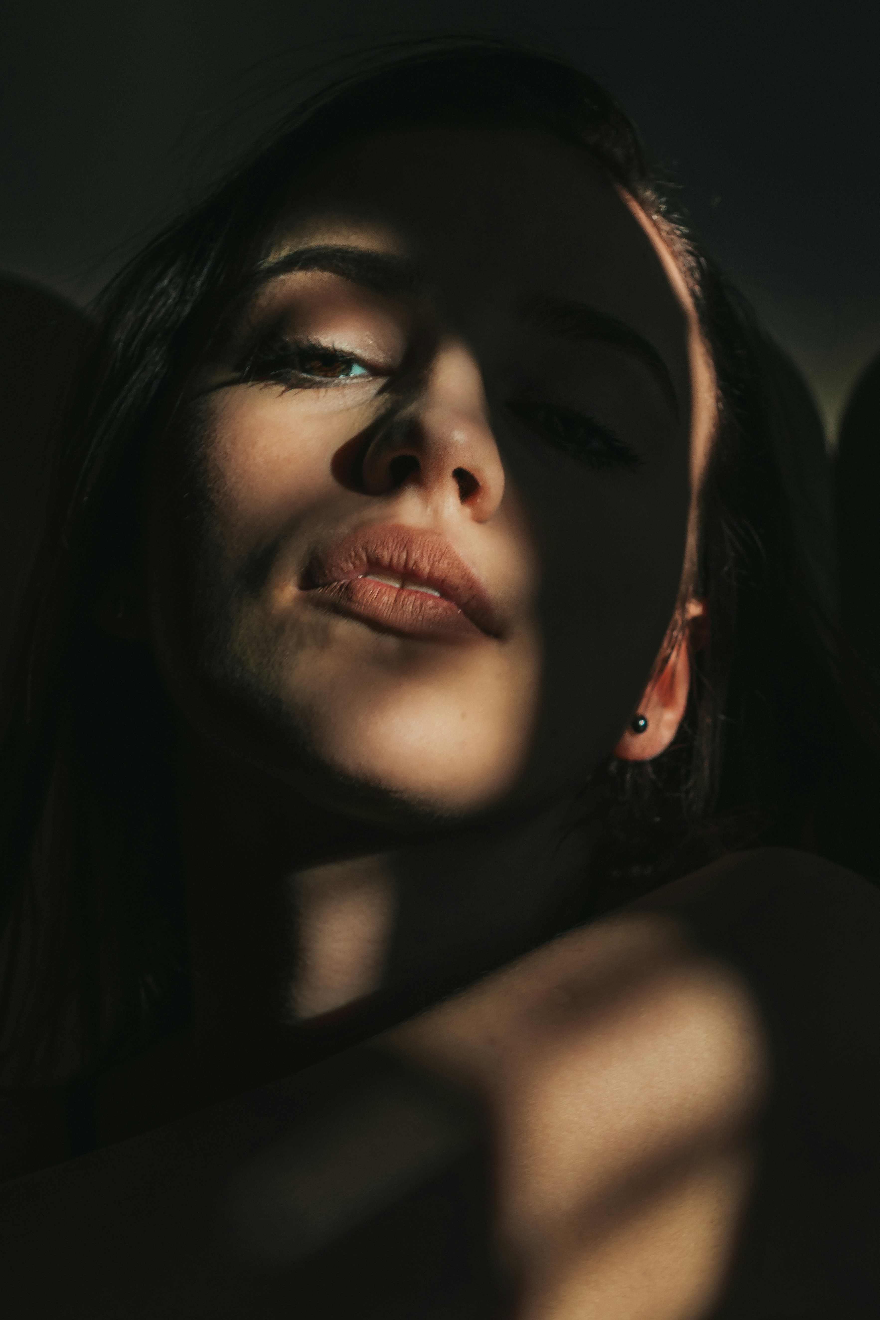 Dramatic lighting illuminates a woman's face with strong shadows.
