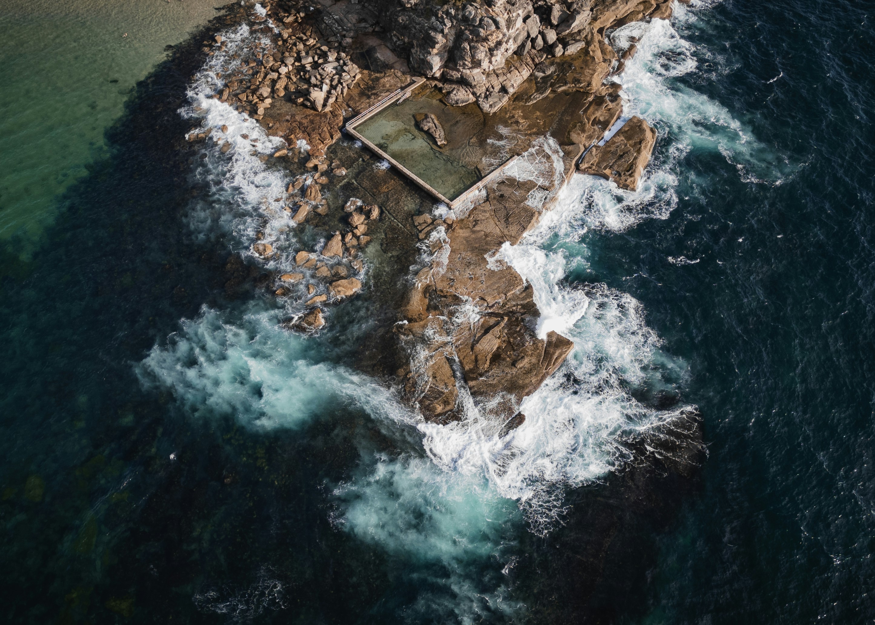 Aerial view of an ocean pool surrounded by crashing waves.