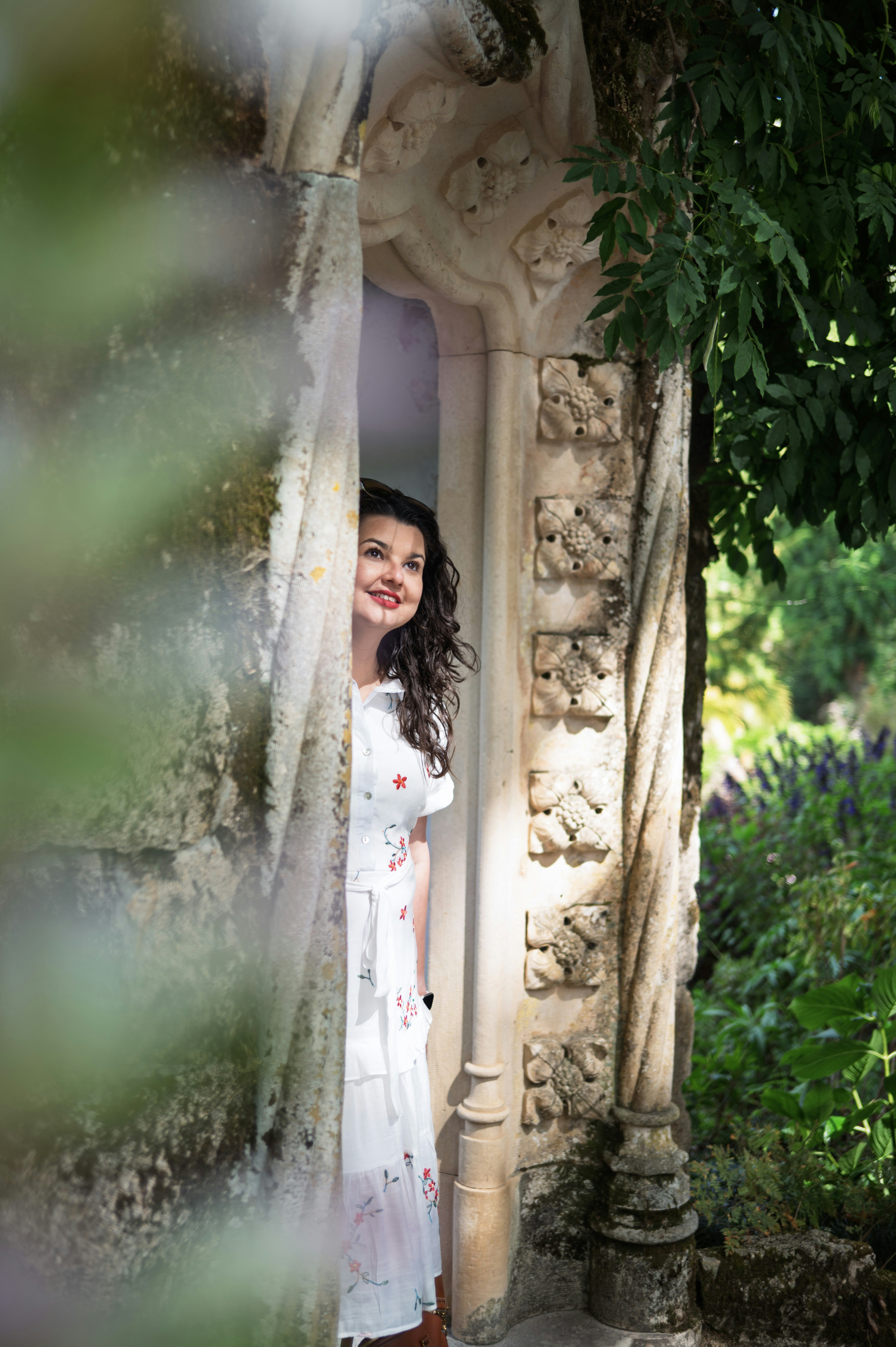 Smiling woman peeking from behind a carved stone archway.
