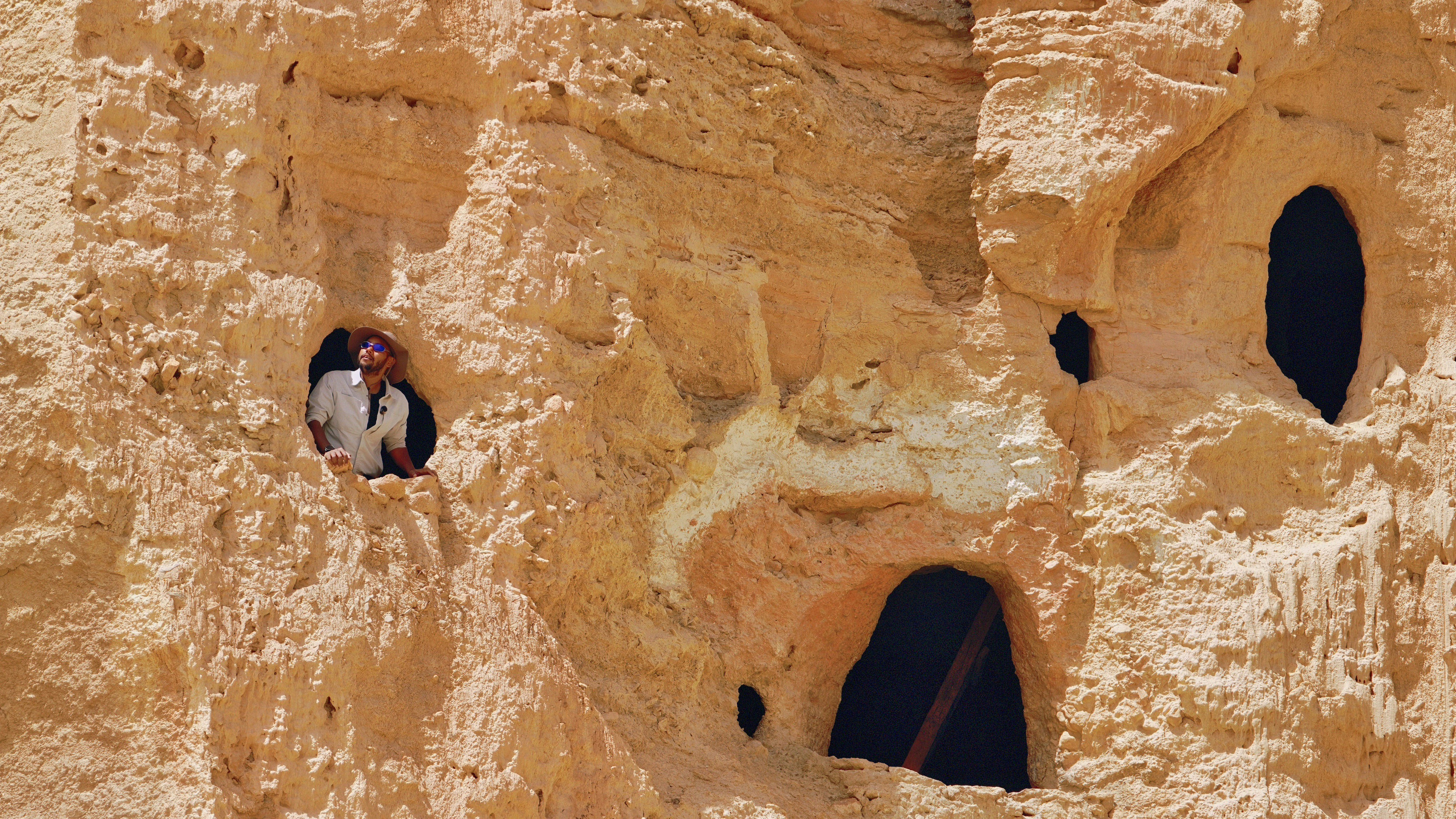 A person in traditional clothes looks out from a cave.