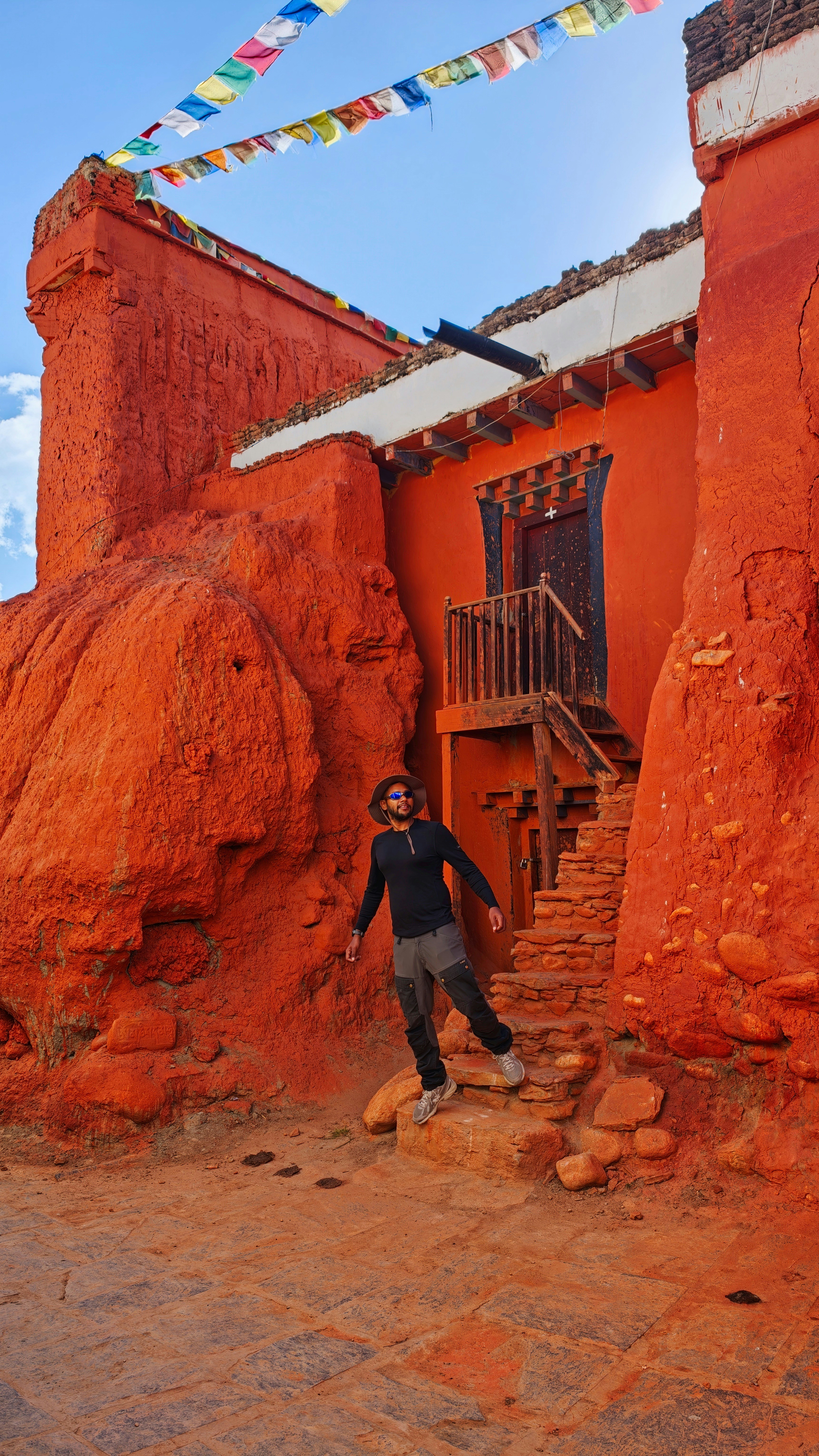 Man on red steps of ancient building with prayer flags.