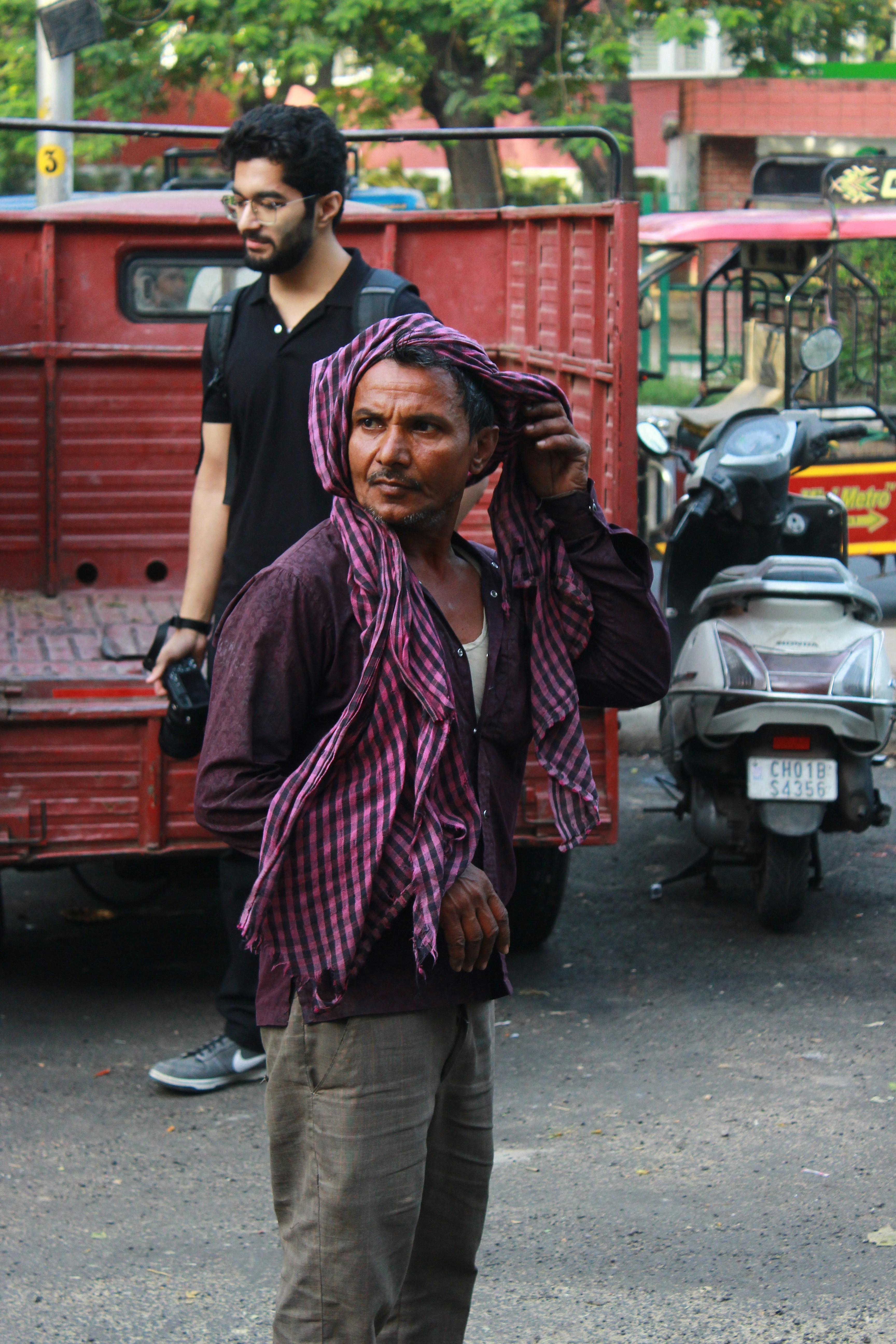 Dusty street portrait: a man adjusting a purple scarf with a curious onlooker in the background