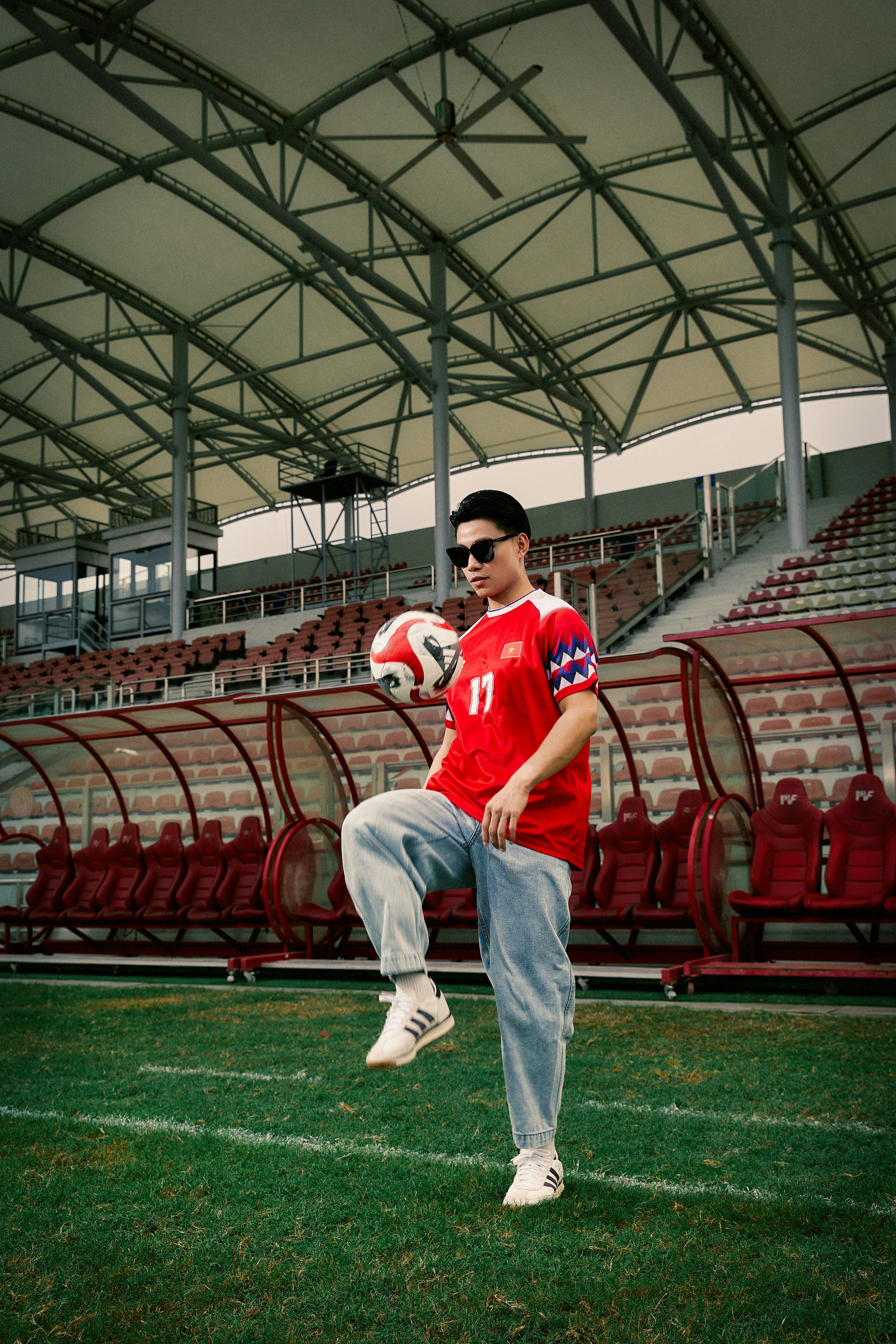 Soccer Athlete in Red Jersey Balancing a Ball on a Stadium Bench