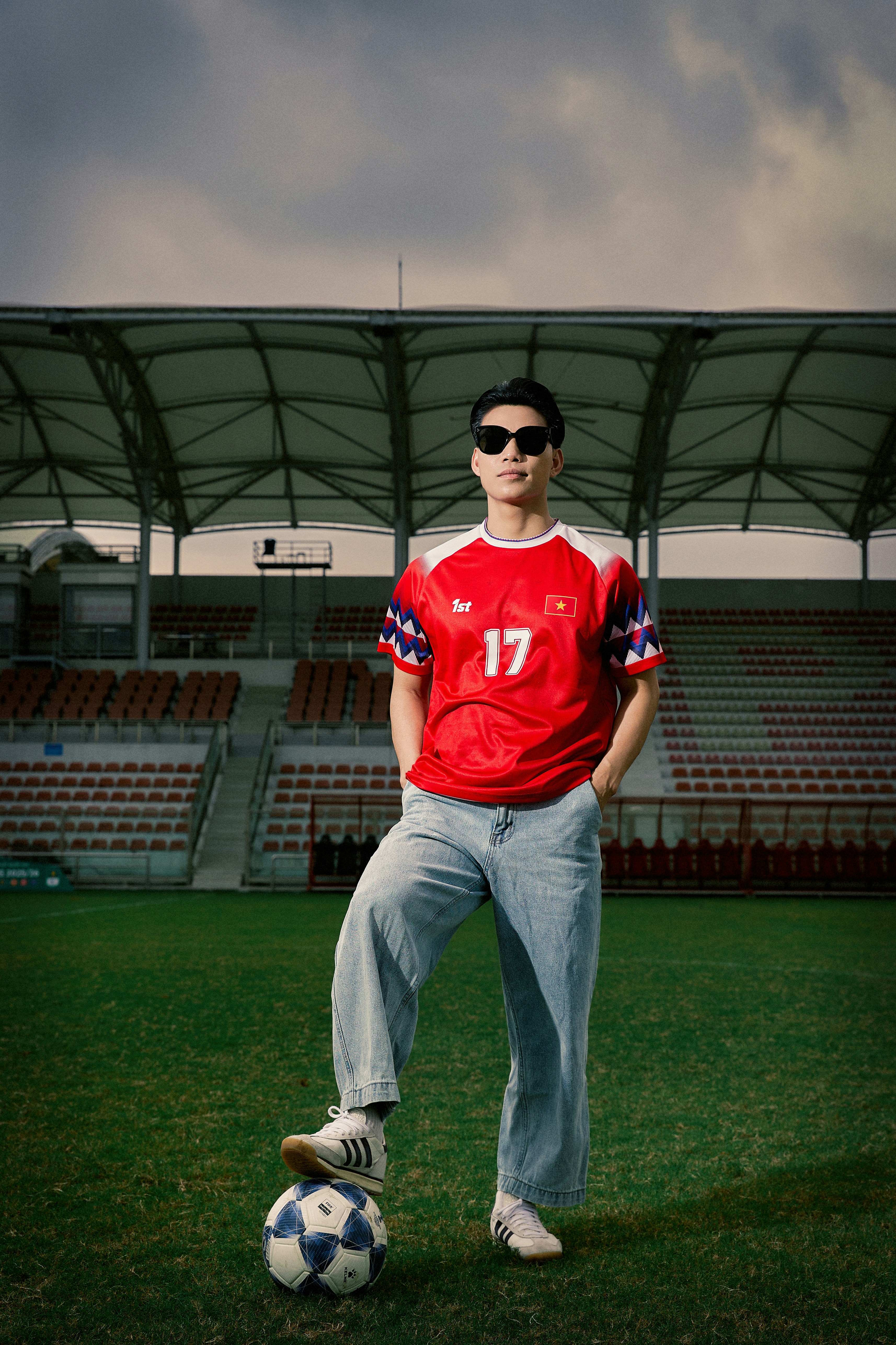 Red-jersey striker stands tall with a soccer ball at his feet in a quiet stadium