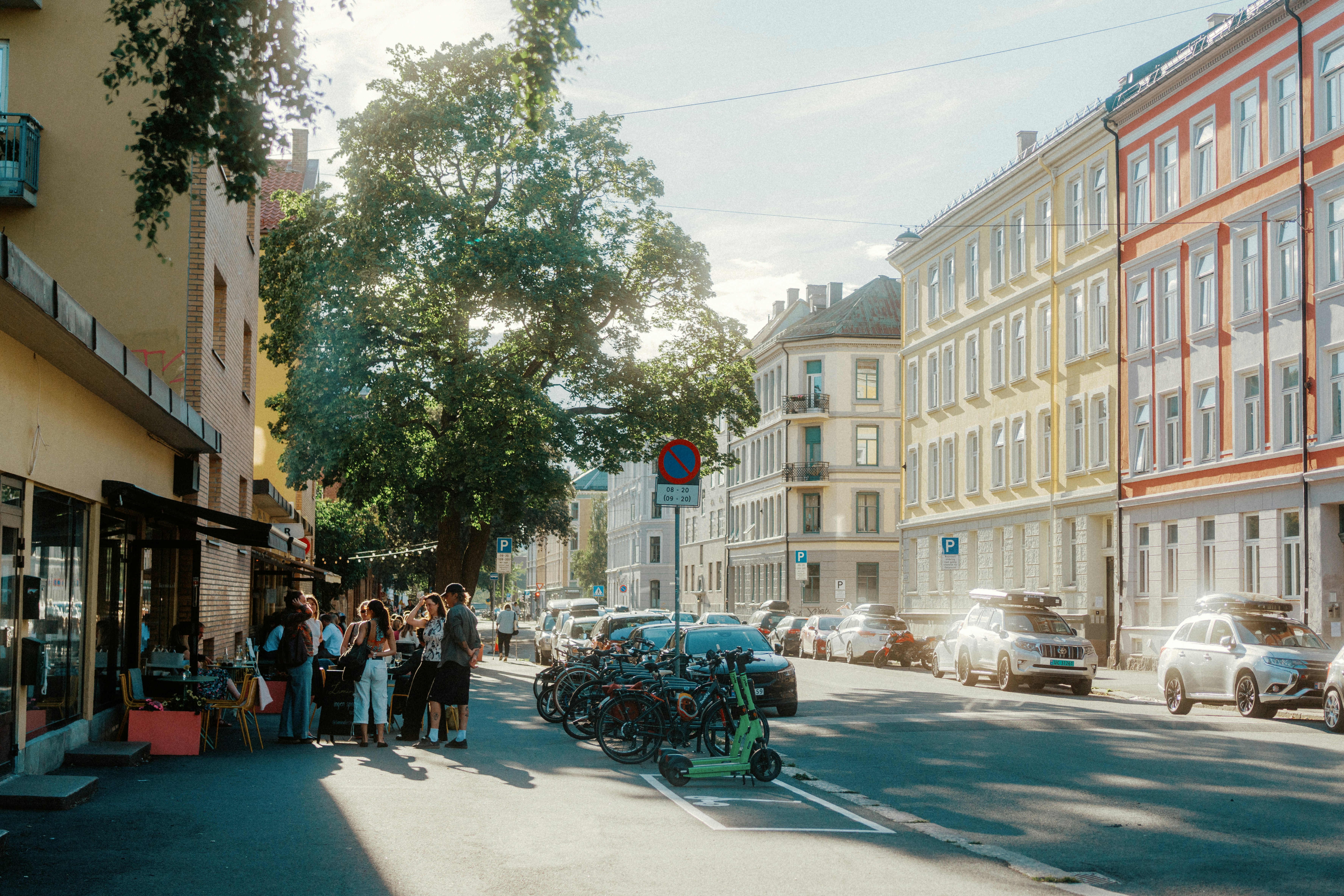 Sunlit Street Scene with Café Fronts and Bikes under a Tree