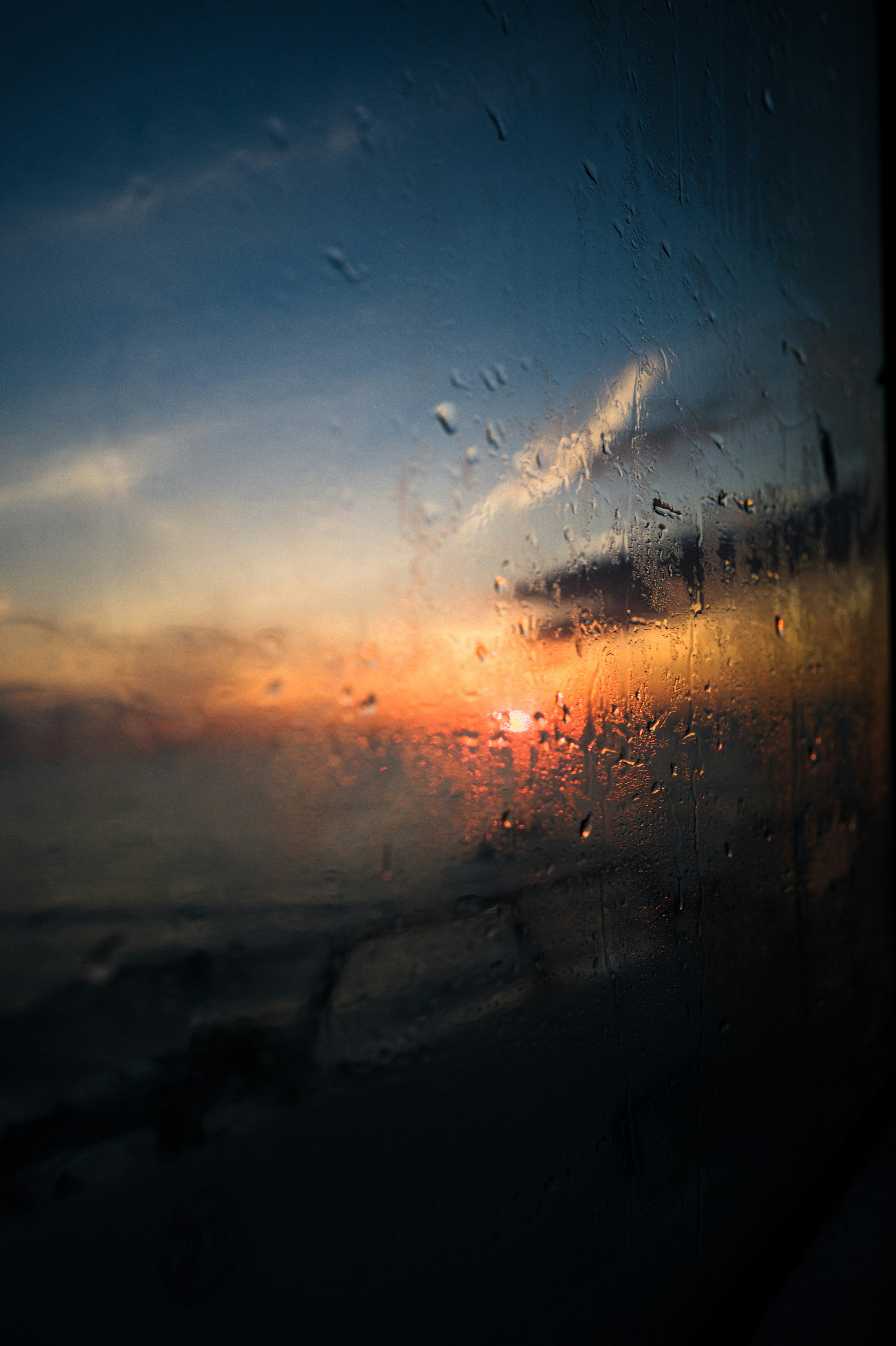 Sunset Through Rain-Streaked Glass Over Coastal Dusk