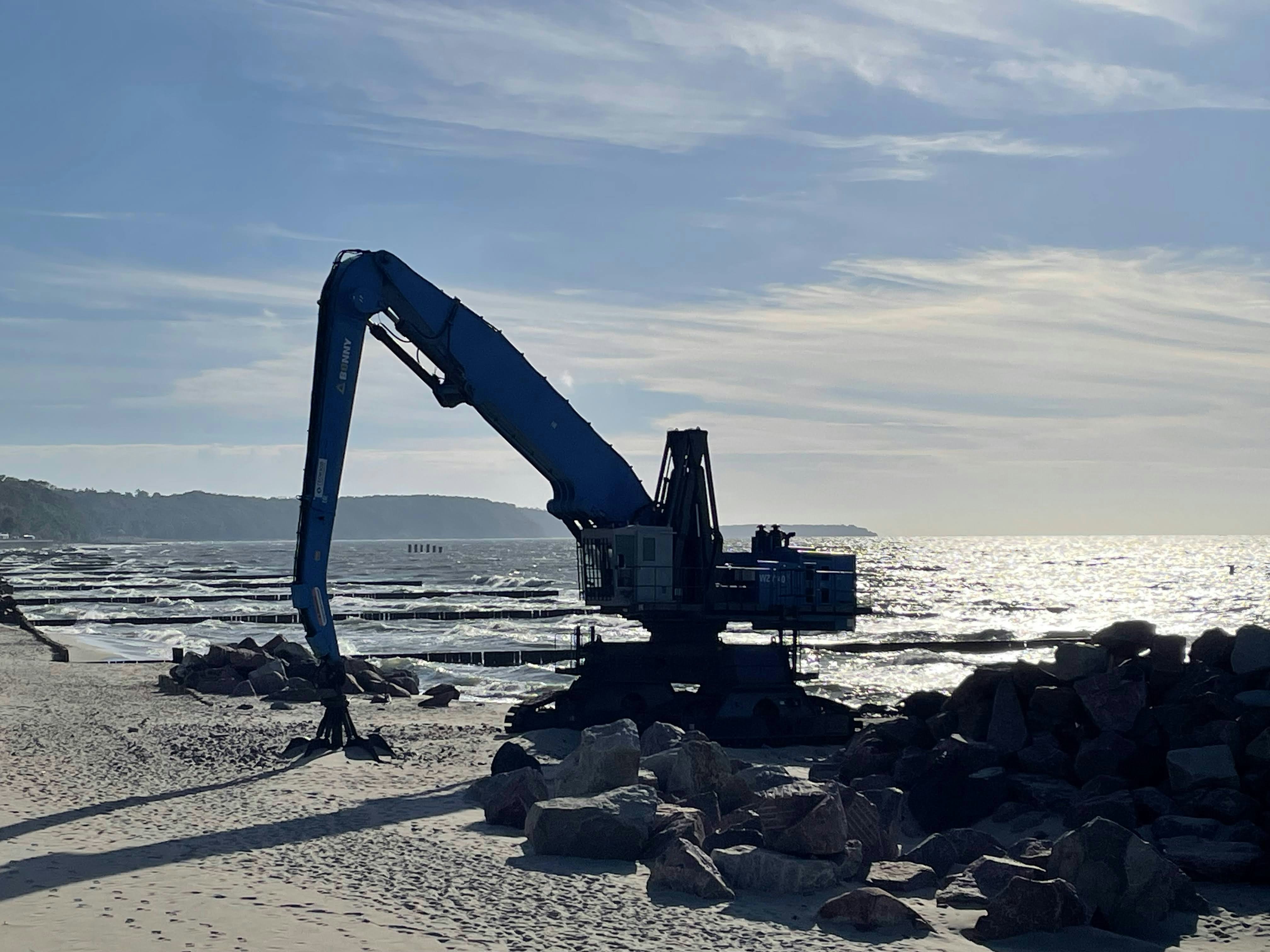 Blue Excavator at Dusk: Seawall Construction by the Shore