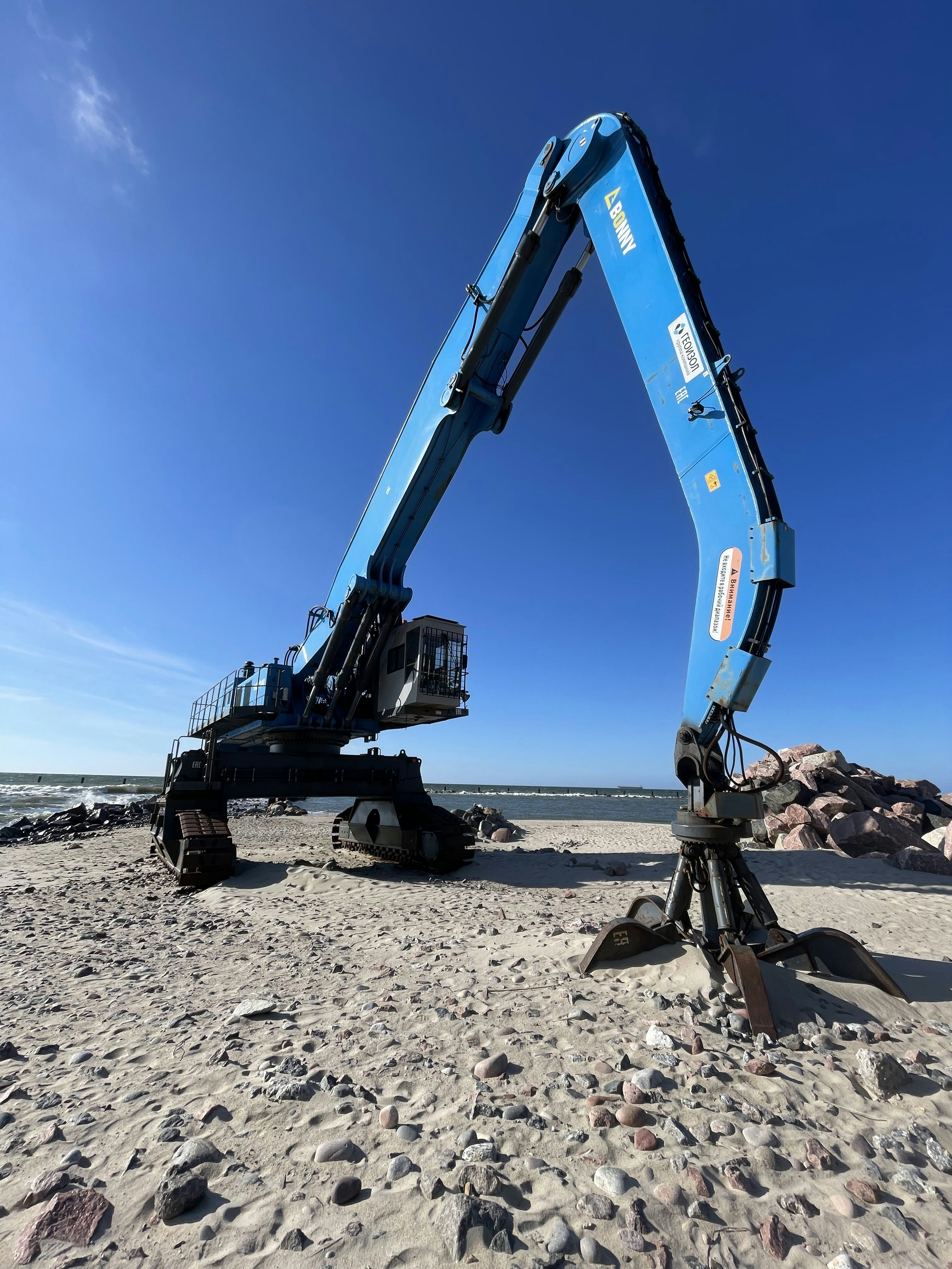 Blue Excavator on a Seaside Rock Shoreline