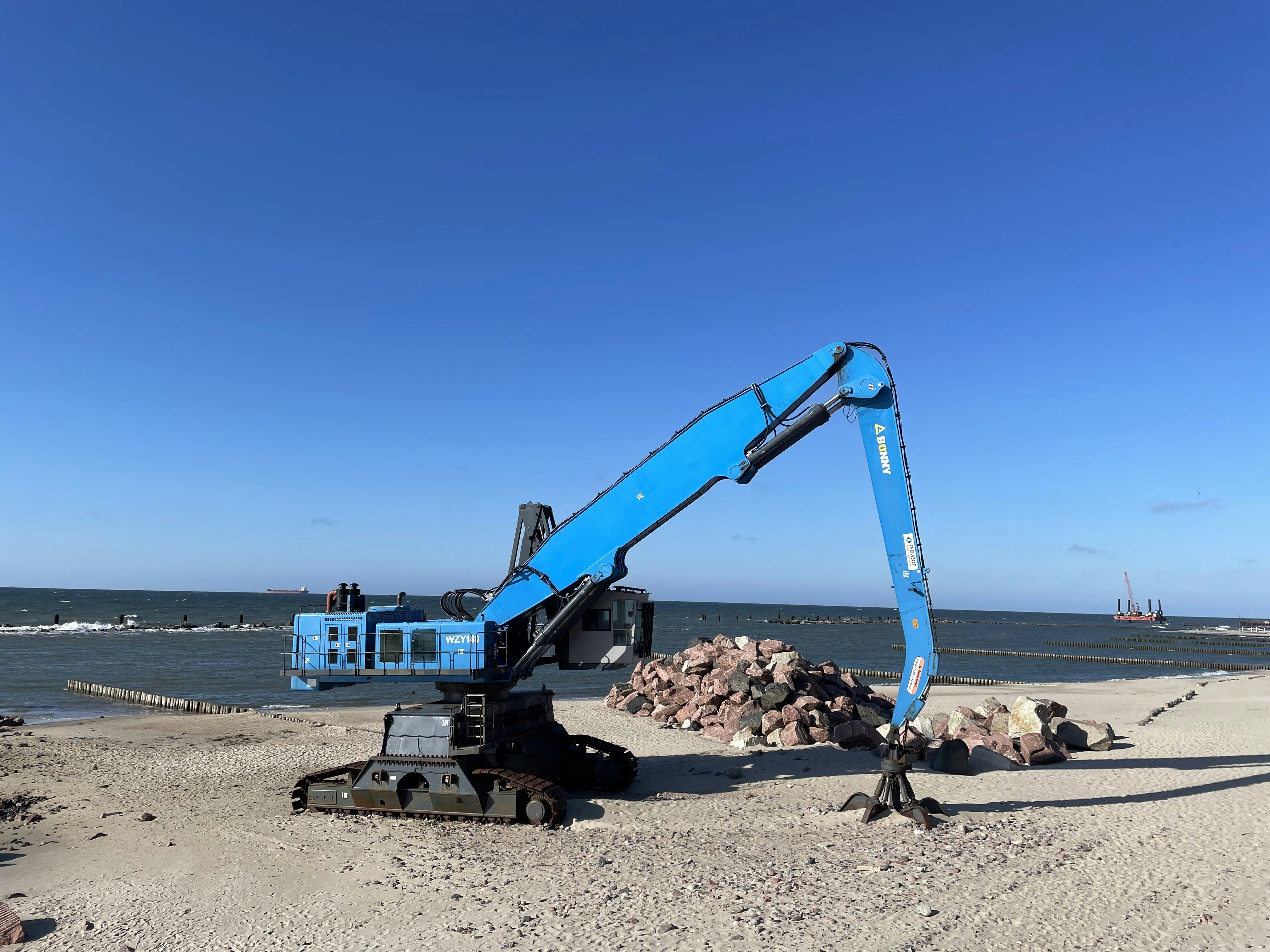 Blue Excavator on a Breeze-washed Beach Reaches for the Sea