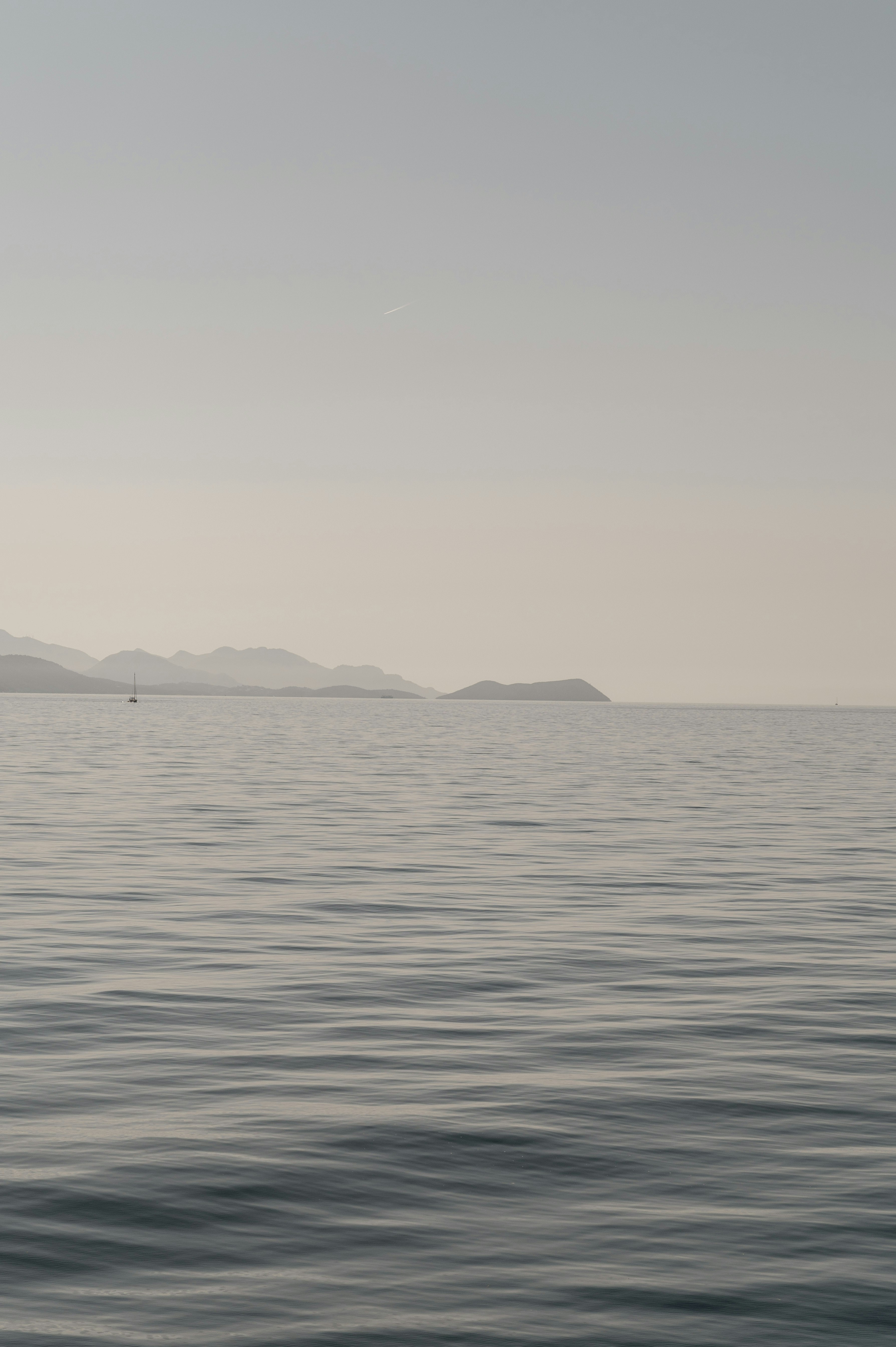 Horizon Quiet: Dusk Over a Calm Sea Beneath Misty Islands