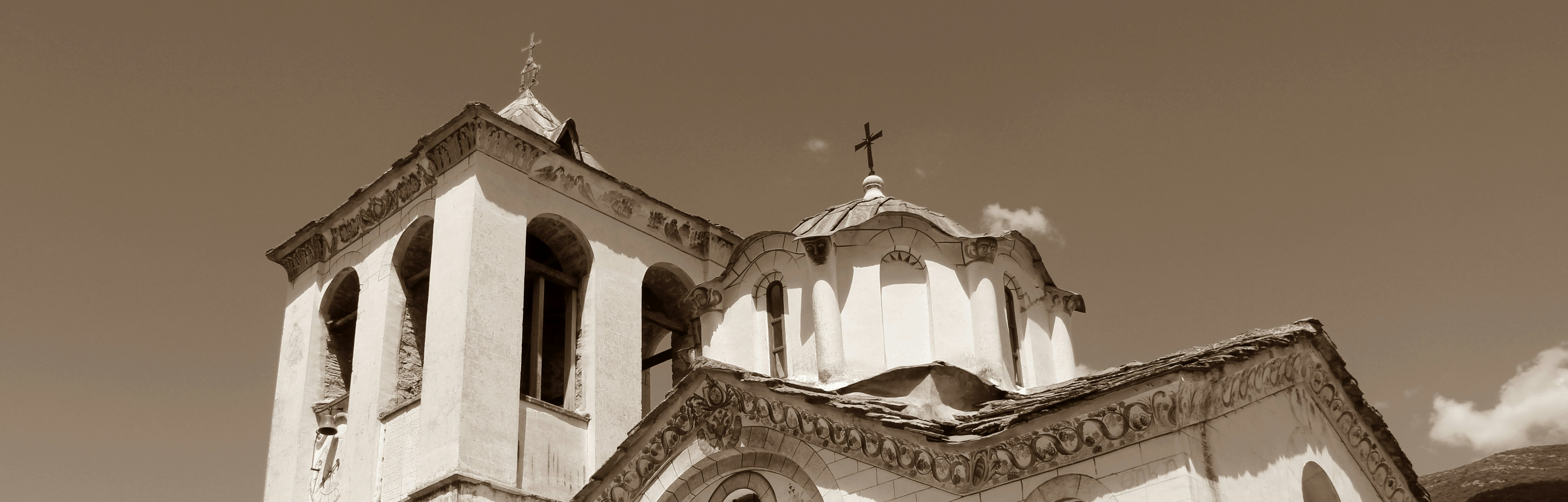 Sepia-toned church tower with domed roof and cross, architectural focus emphasizing the aged façade and classical arches.