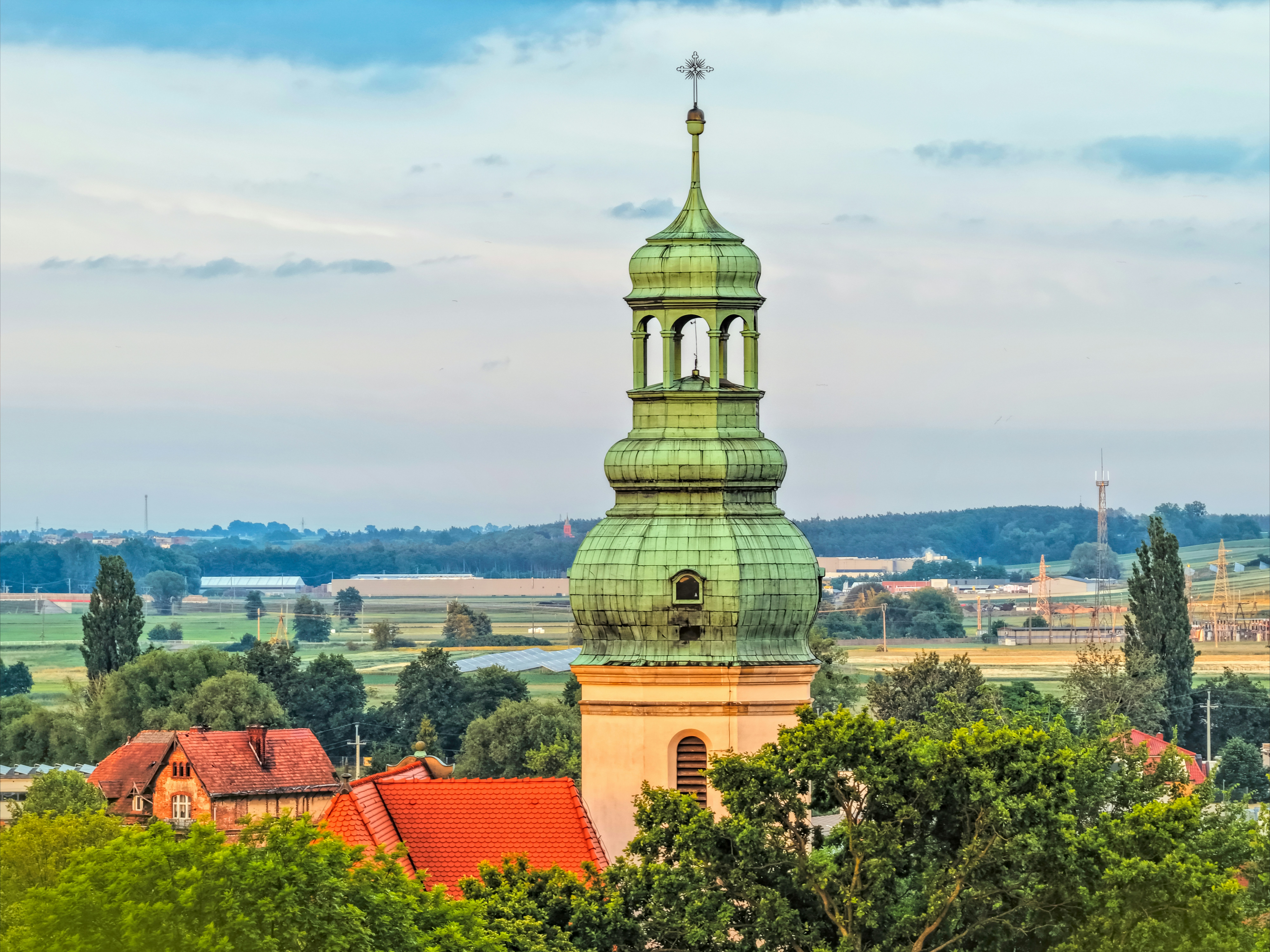 Green steeple amid red-tiled roofs: a village church under a wide sky