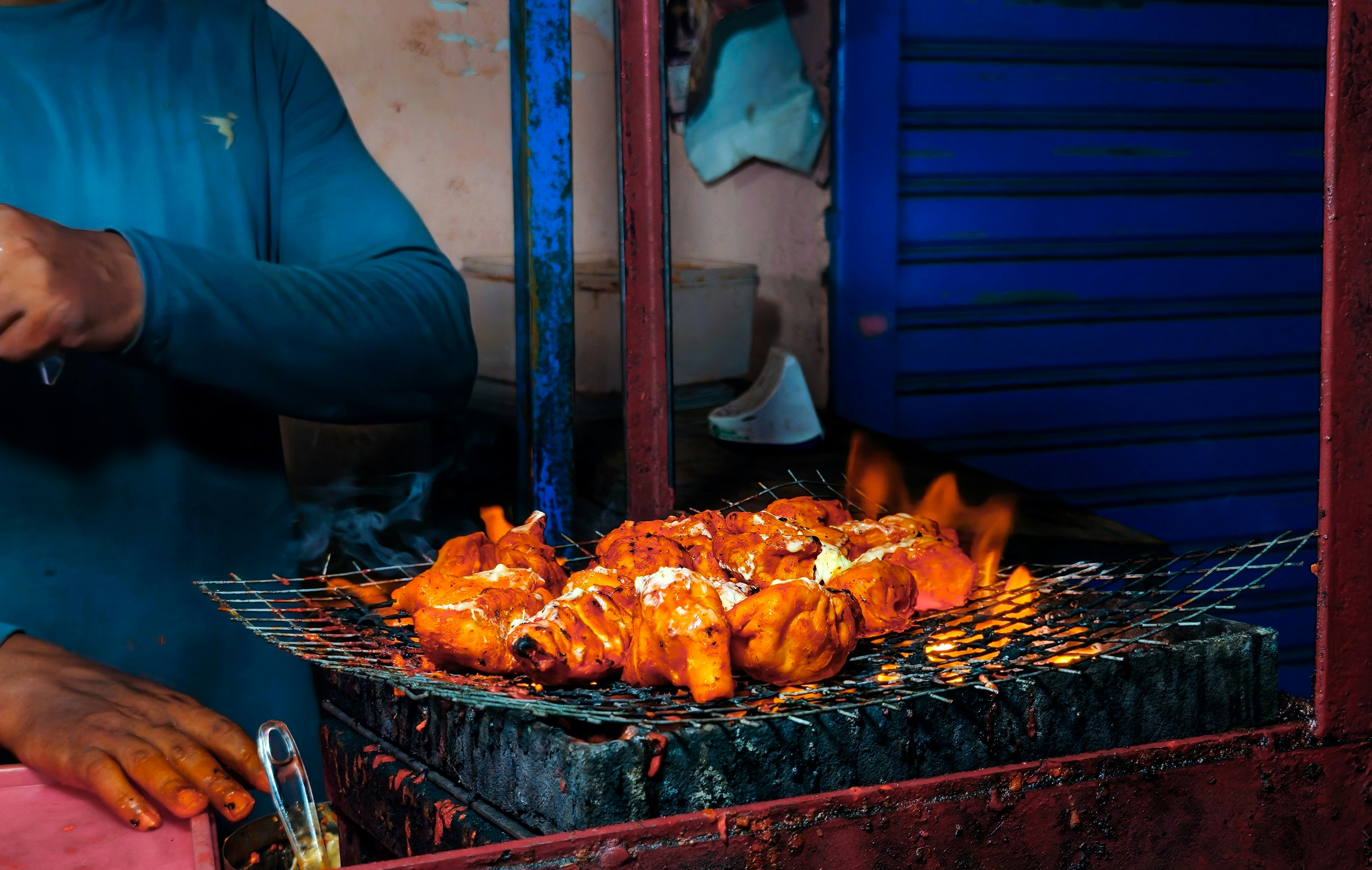 A person grilling chicken with flames on a charcoal grill.