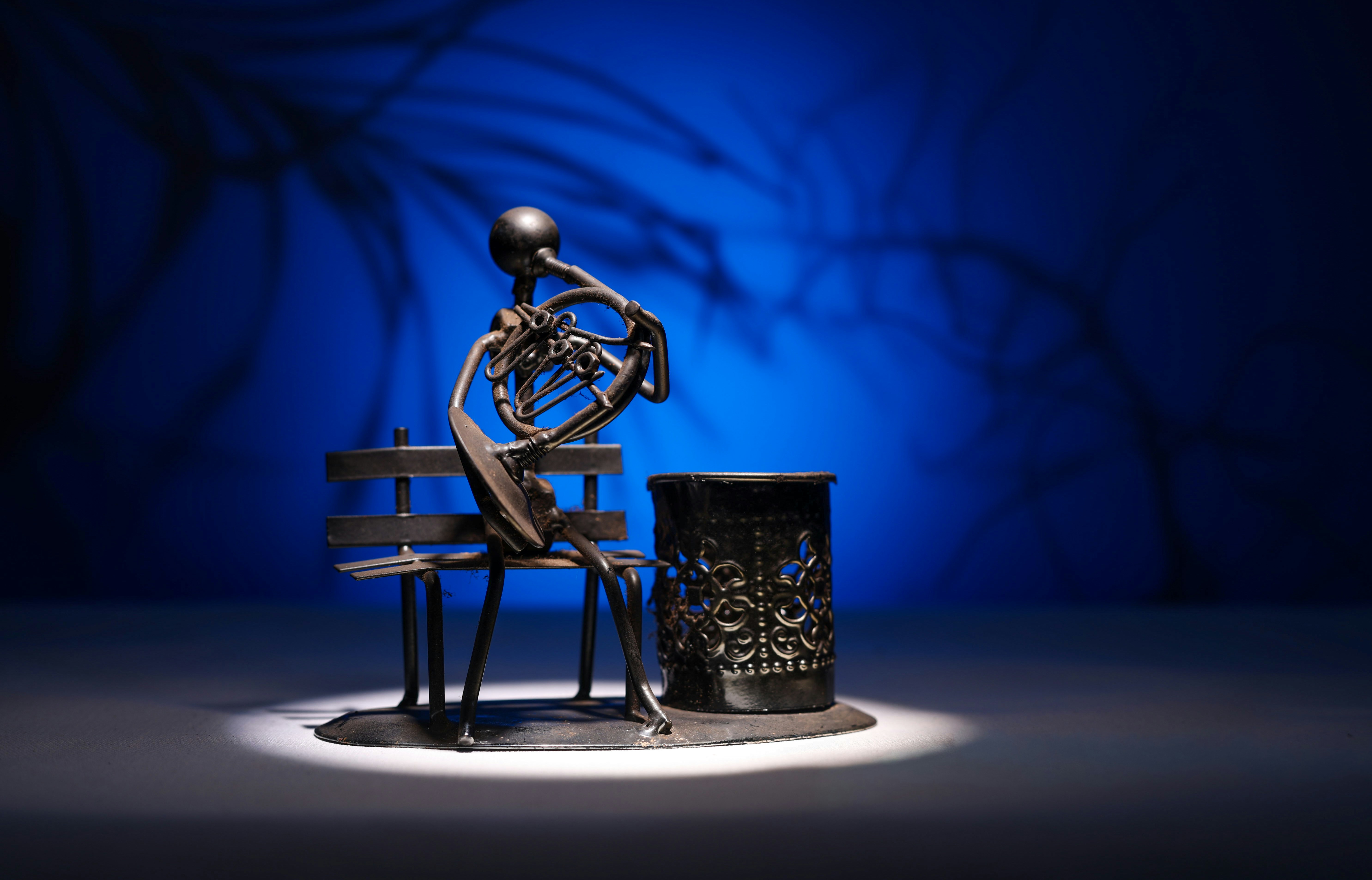 Metal Figure on a Bench Finds Shade by a Cylindrical Ornament