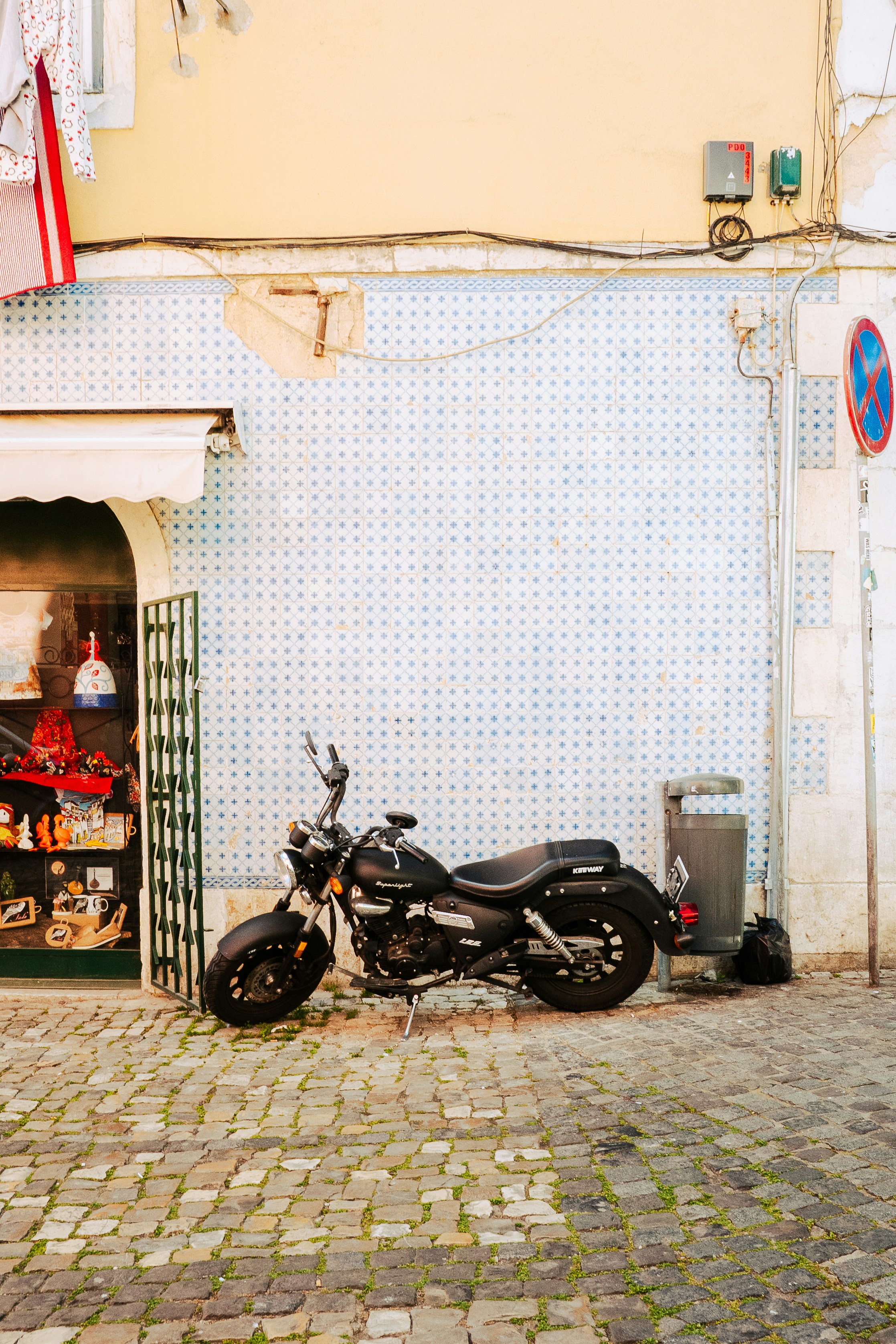 Black Motorcycle Resting Against a Pale-Blue Tile Facade
