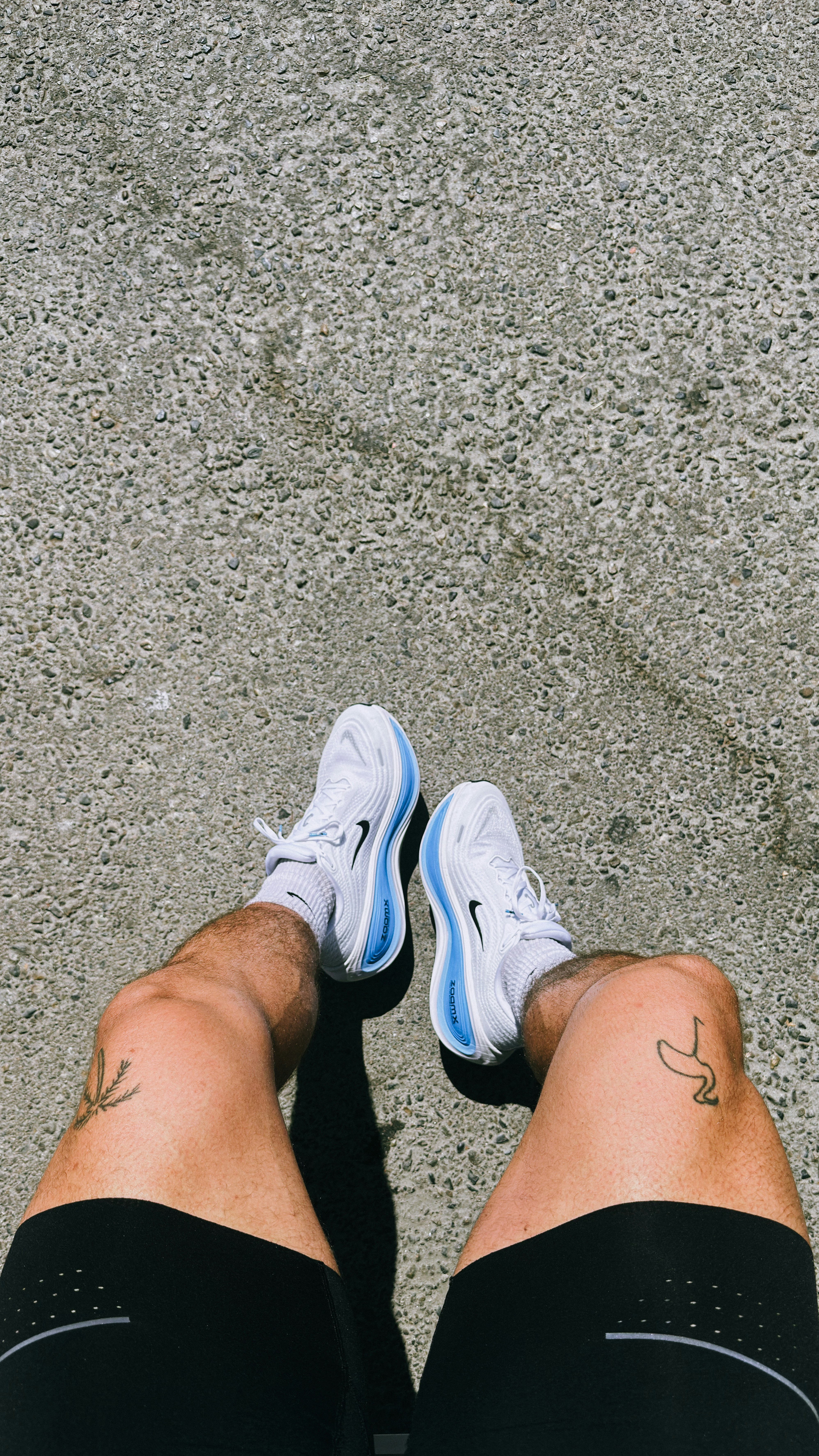 Centered stride: white sneakers and tattooed knees on sunlit pavement