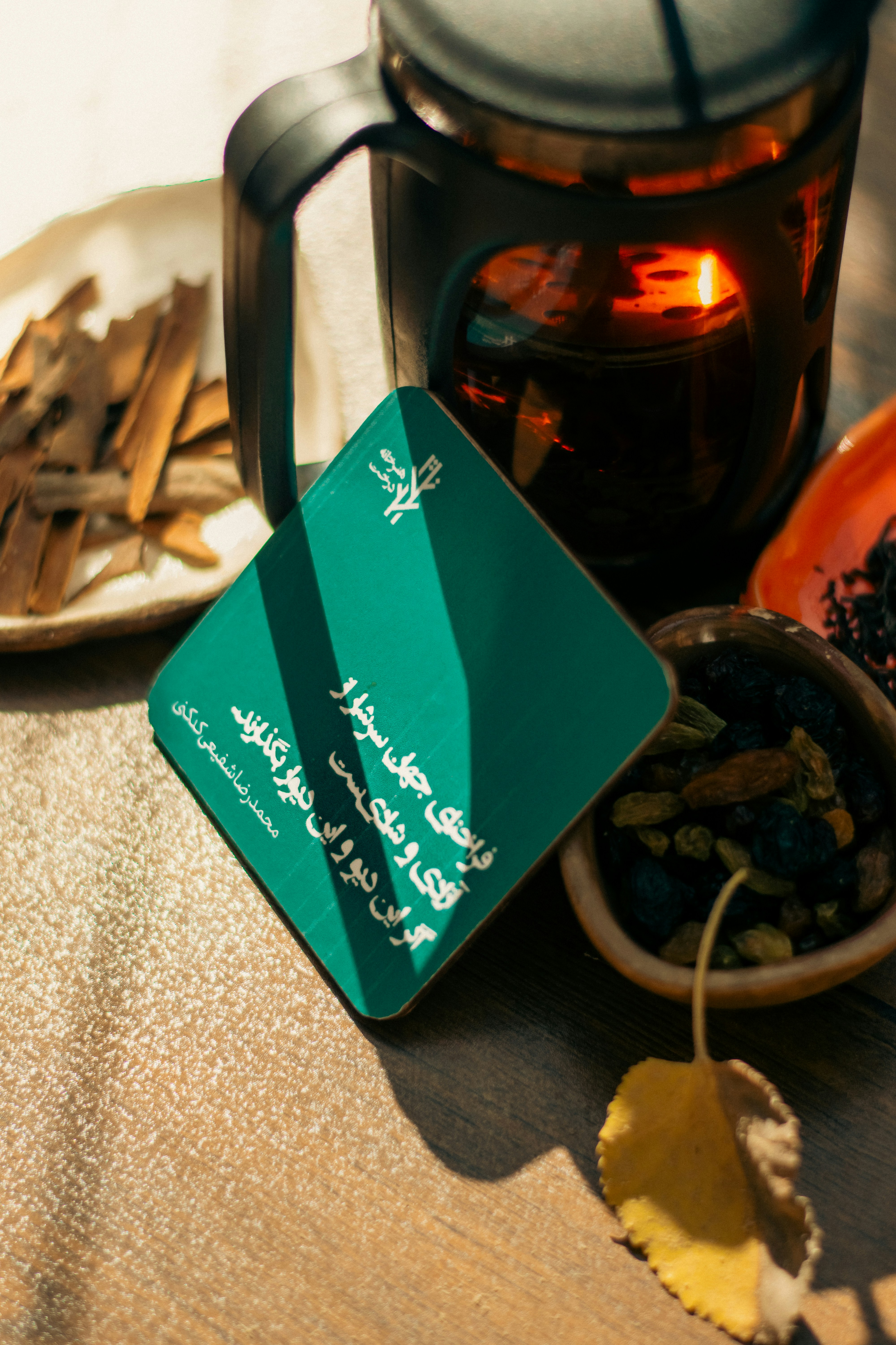 Teal card rests against a coffee pot, catching warm sunlight