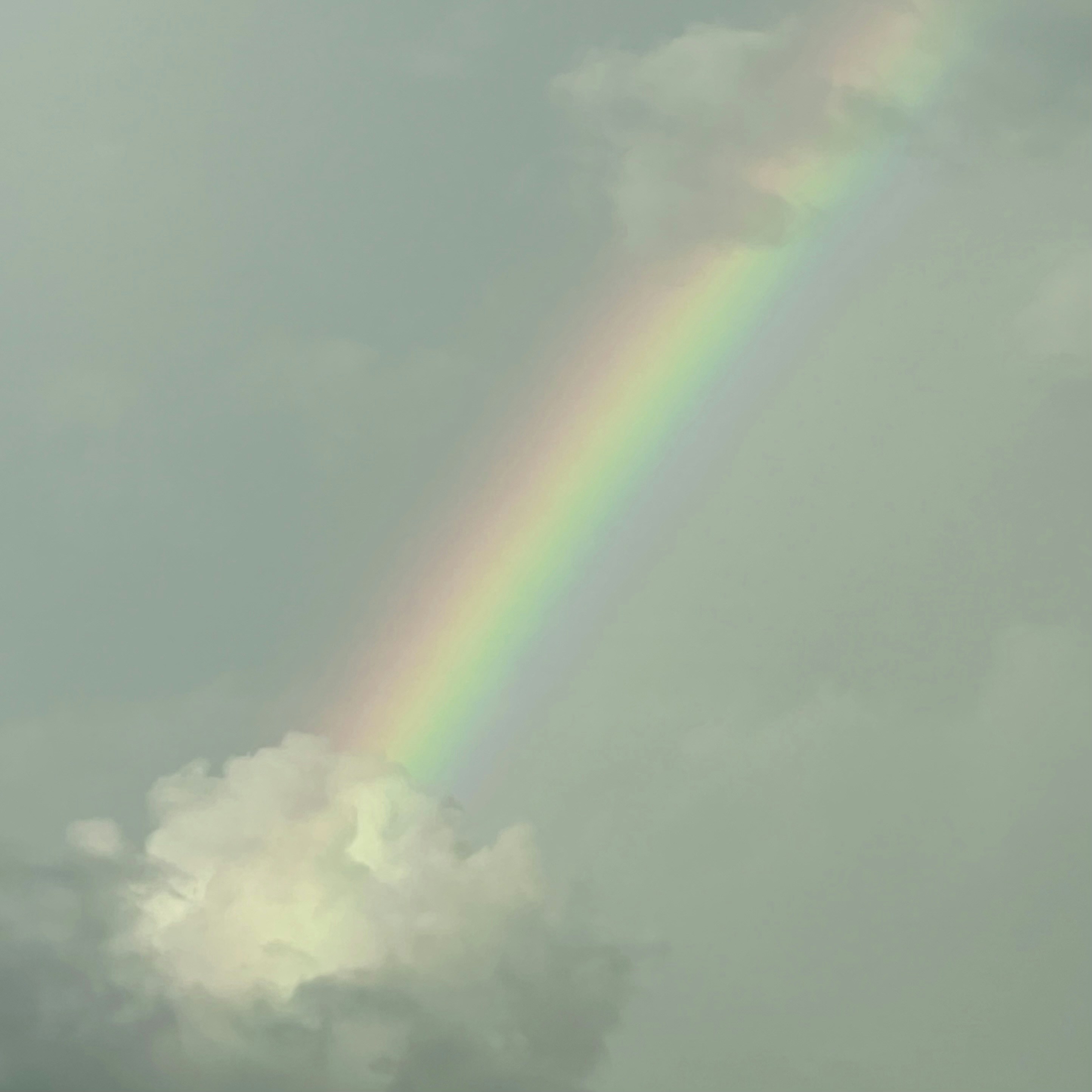 Vivid rainbow arcs across a pale sky above gentle cloud outlines.