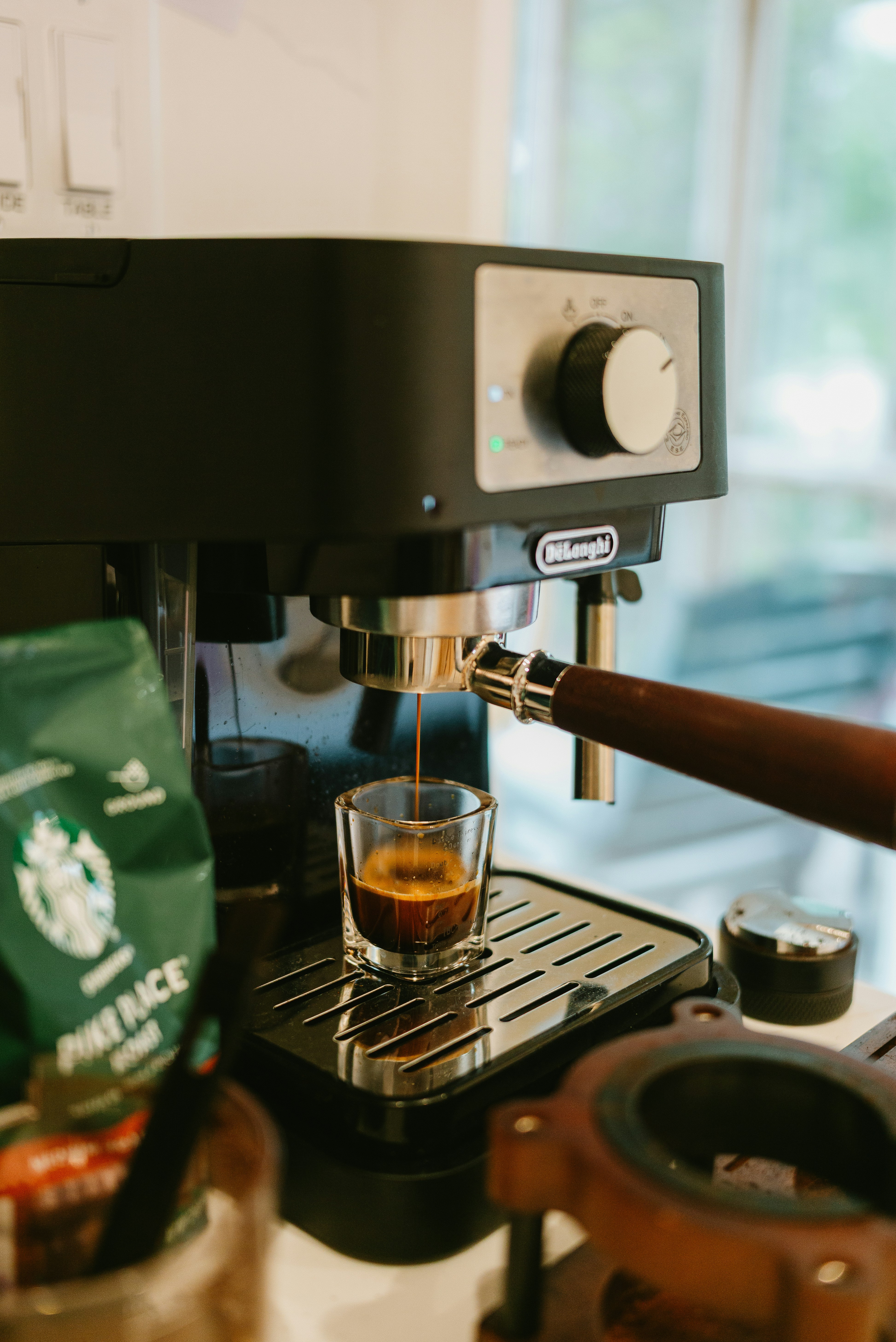 Coffee machine releasing a shot into a glass, with beans and cups surrounding the espresso setup in a cozy kitchen scene.