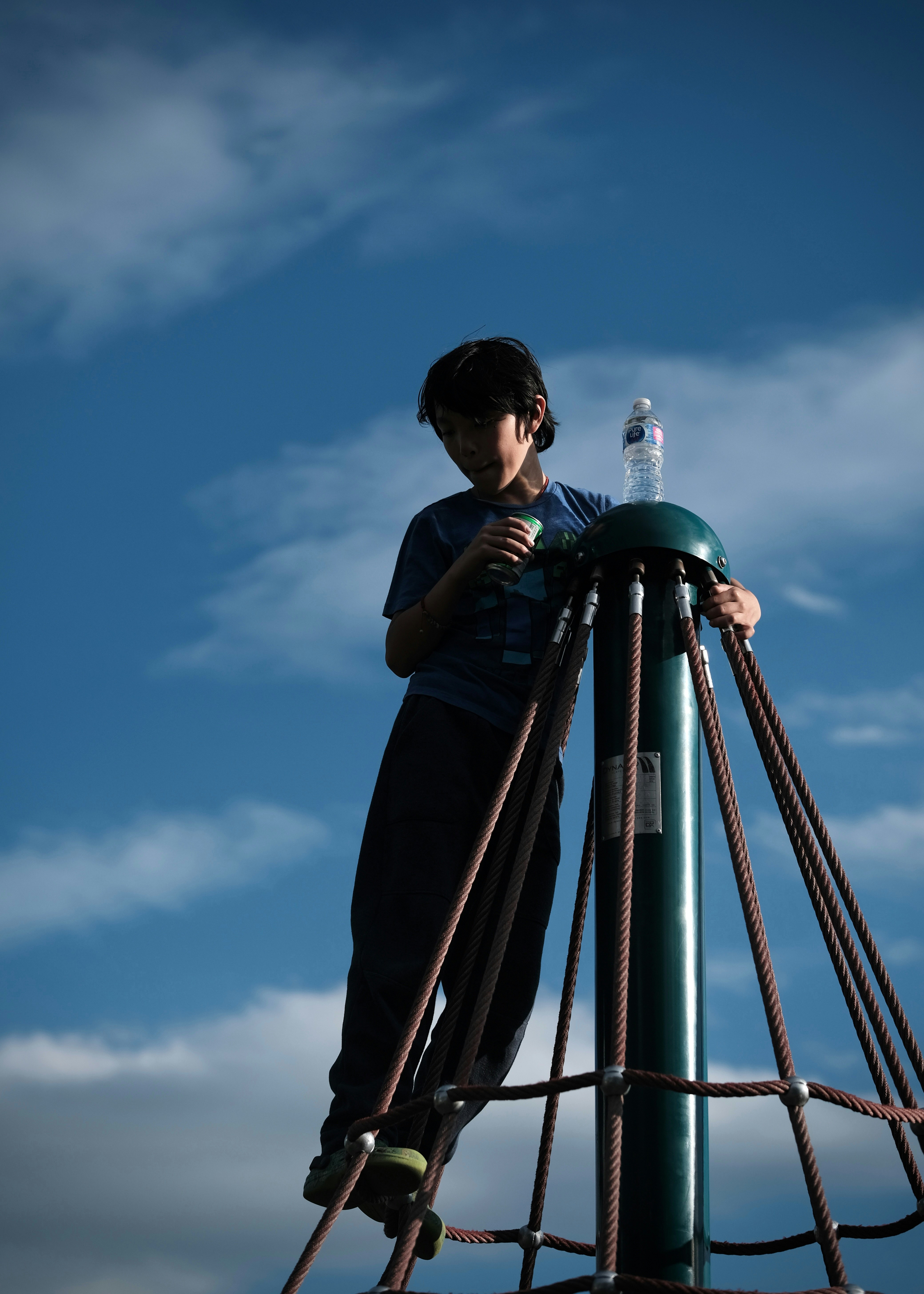 Careful climber at the top: a boy and the rope tower against the blue sky