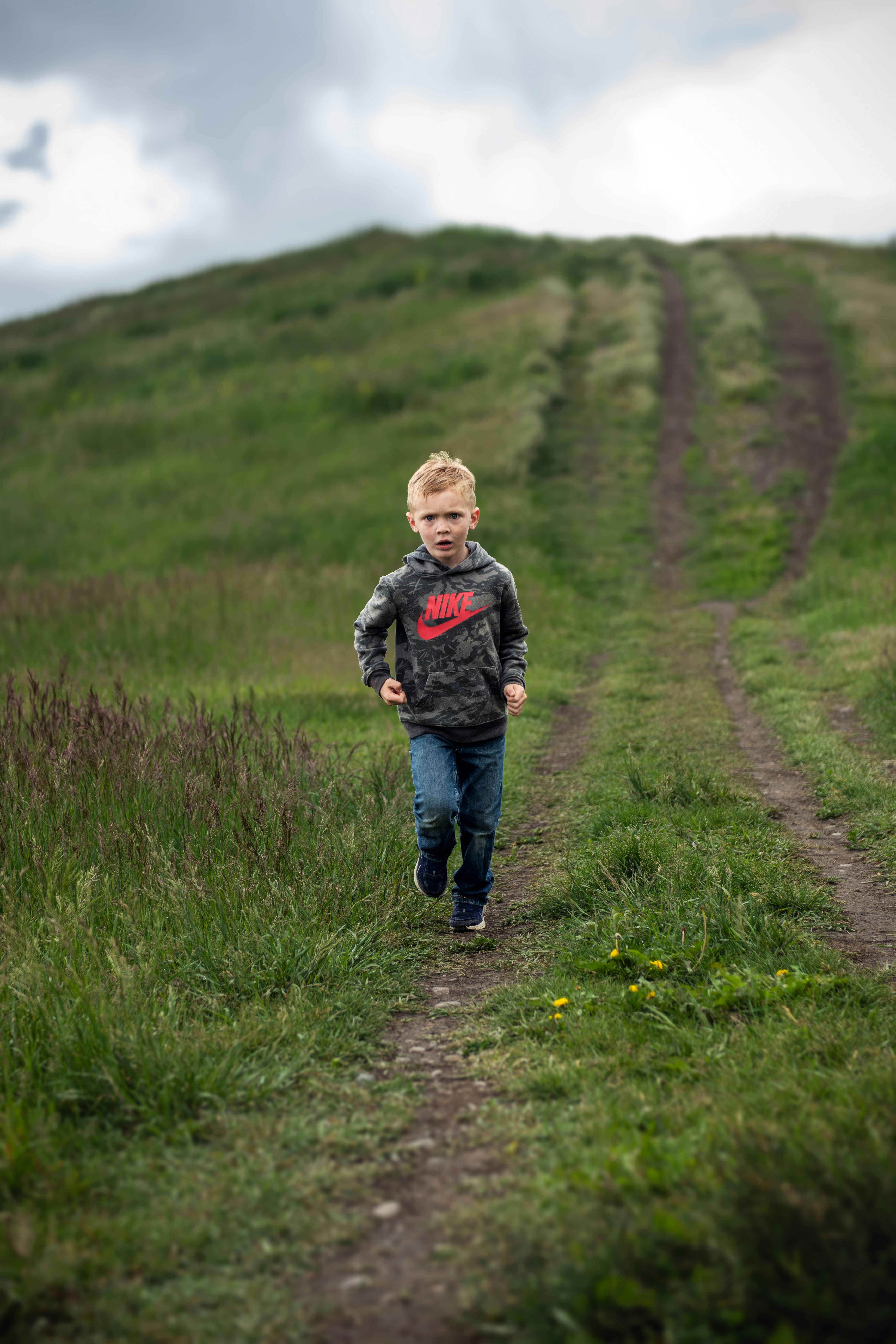 Lone sprint toward the hill: a boy questing up a grassy trail