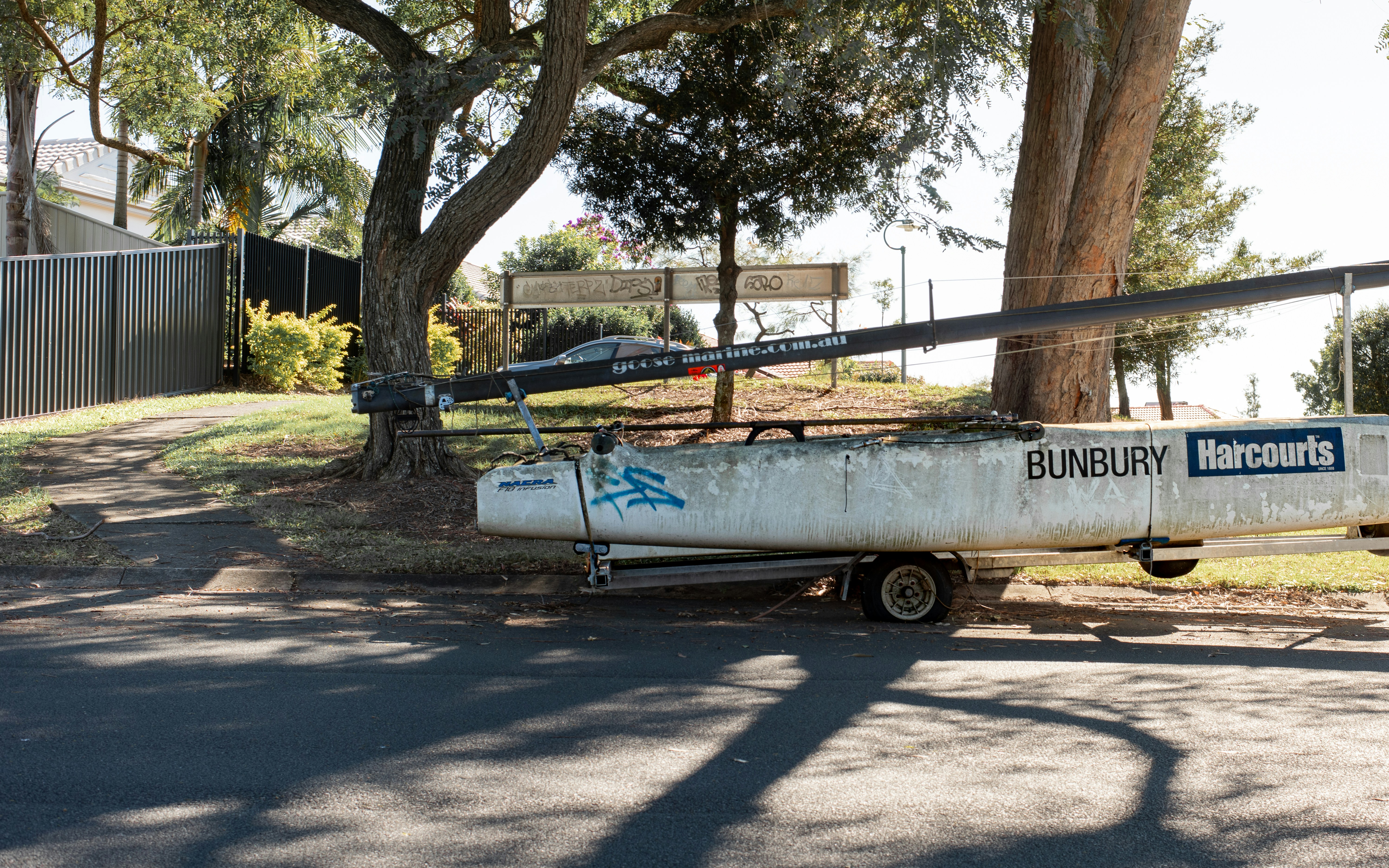 Weathered boat trailer under dappled shade near a quiet street