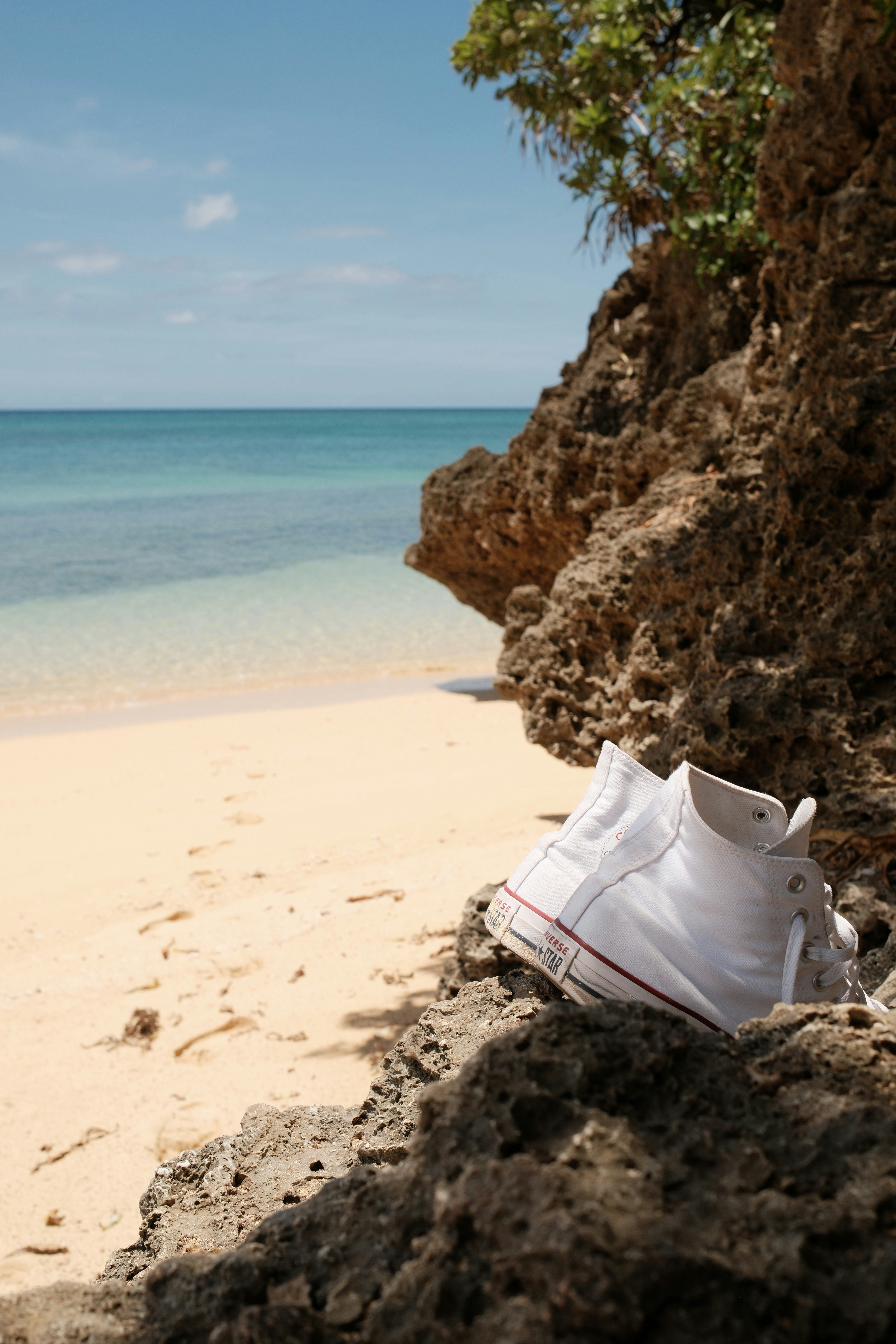 White sneakers resting on coastal rock with turquoise sea