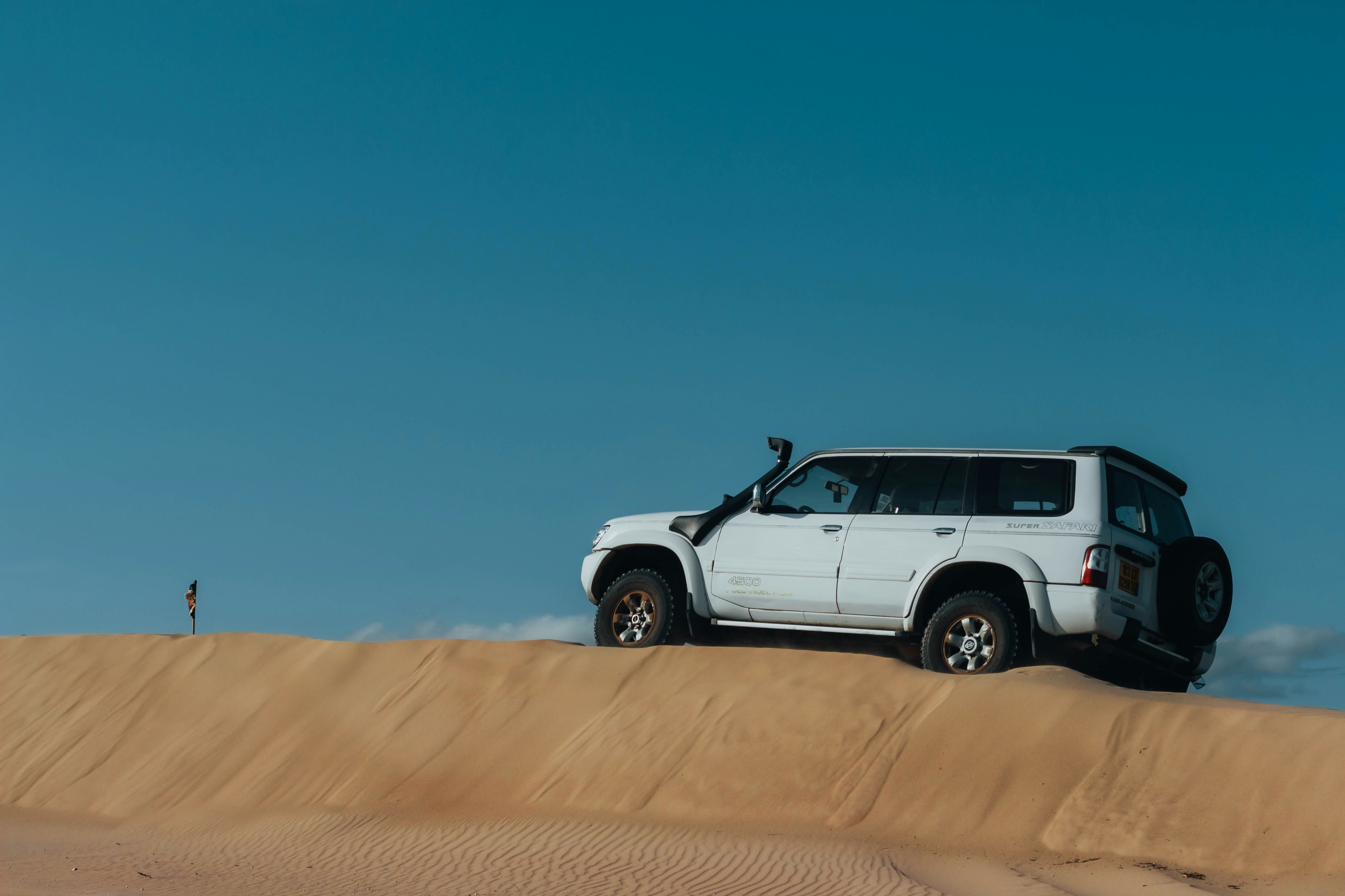 Desert Patrol: White SUV Climbing a Sand Dune Under a Clear Blue Sky