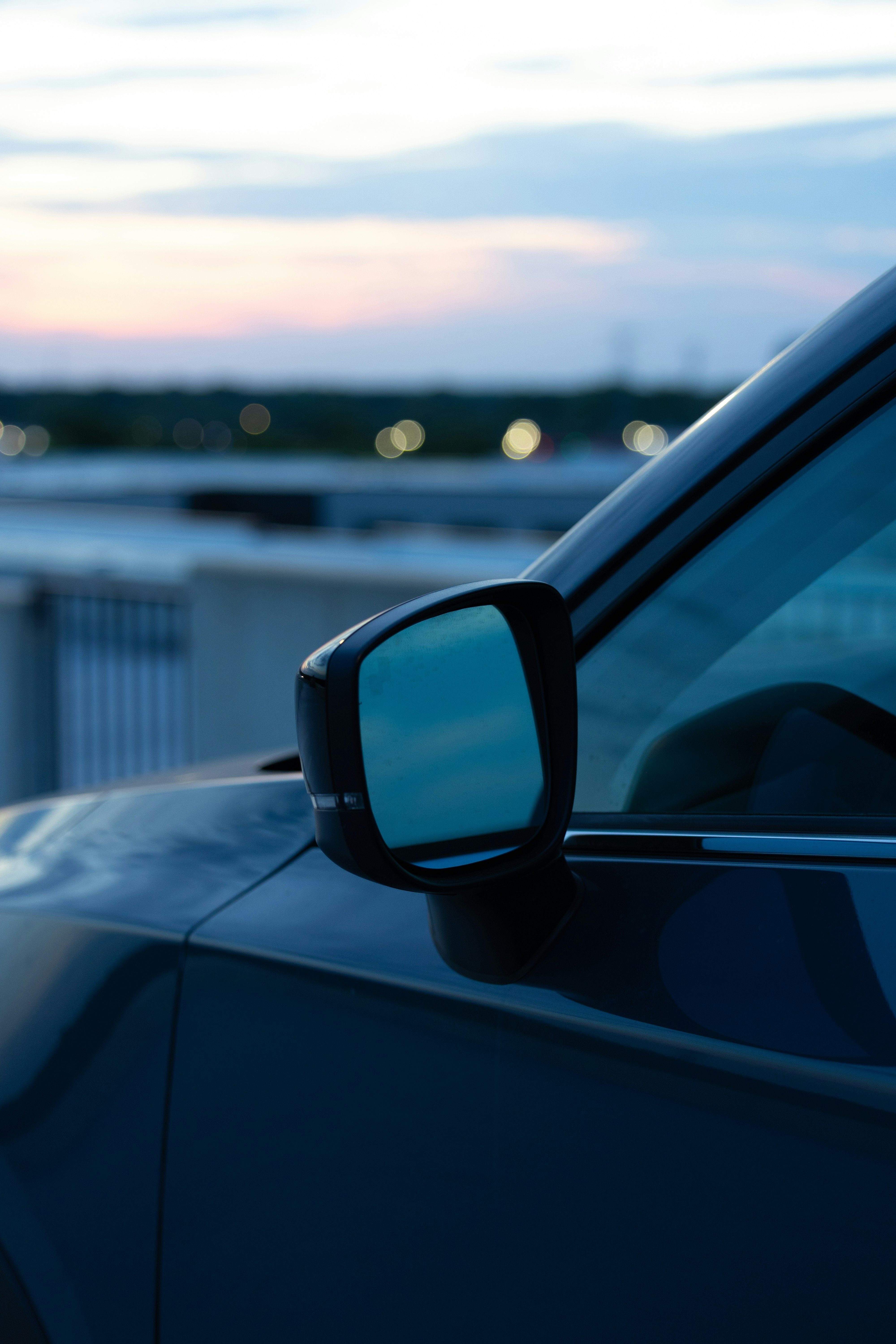 Close-up of a car side mirror at dusk with city lights in the distance