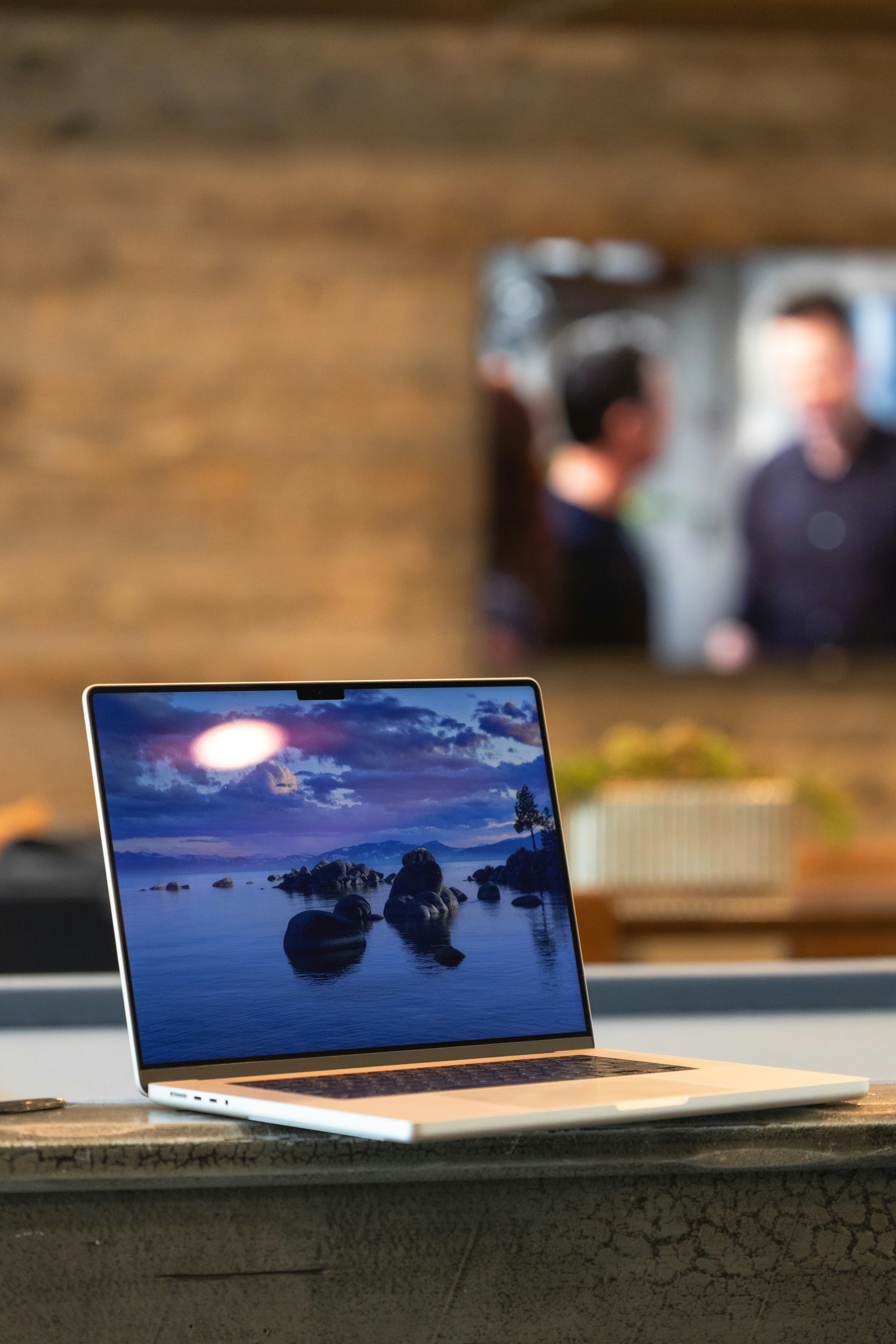Laptop on a Rustic Bar Counter Reflects a Blurred TV Scene