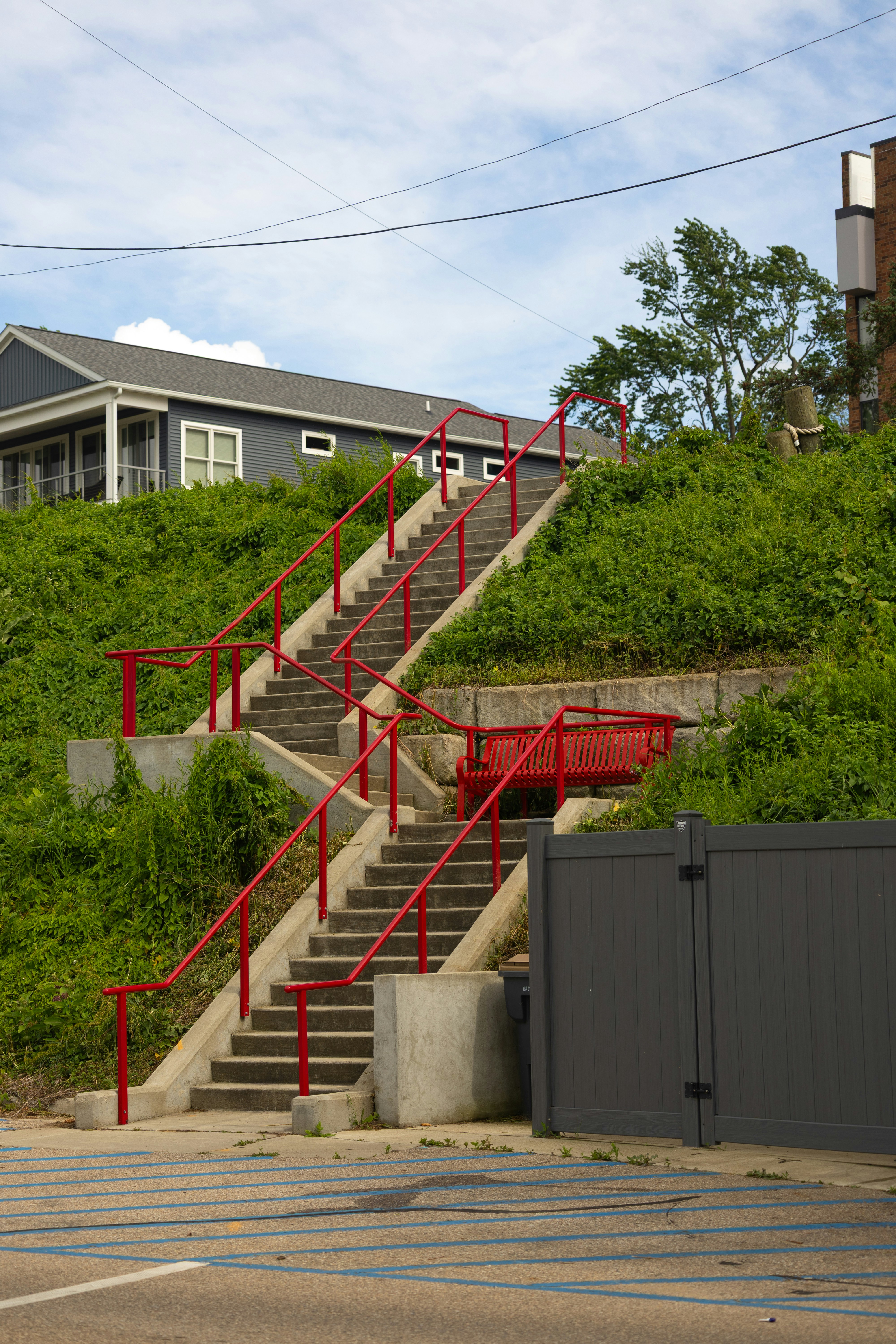 Red Staircase Ascending Through Greenery Beneath a Suburban Crest