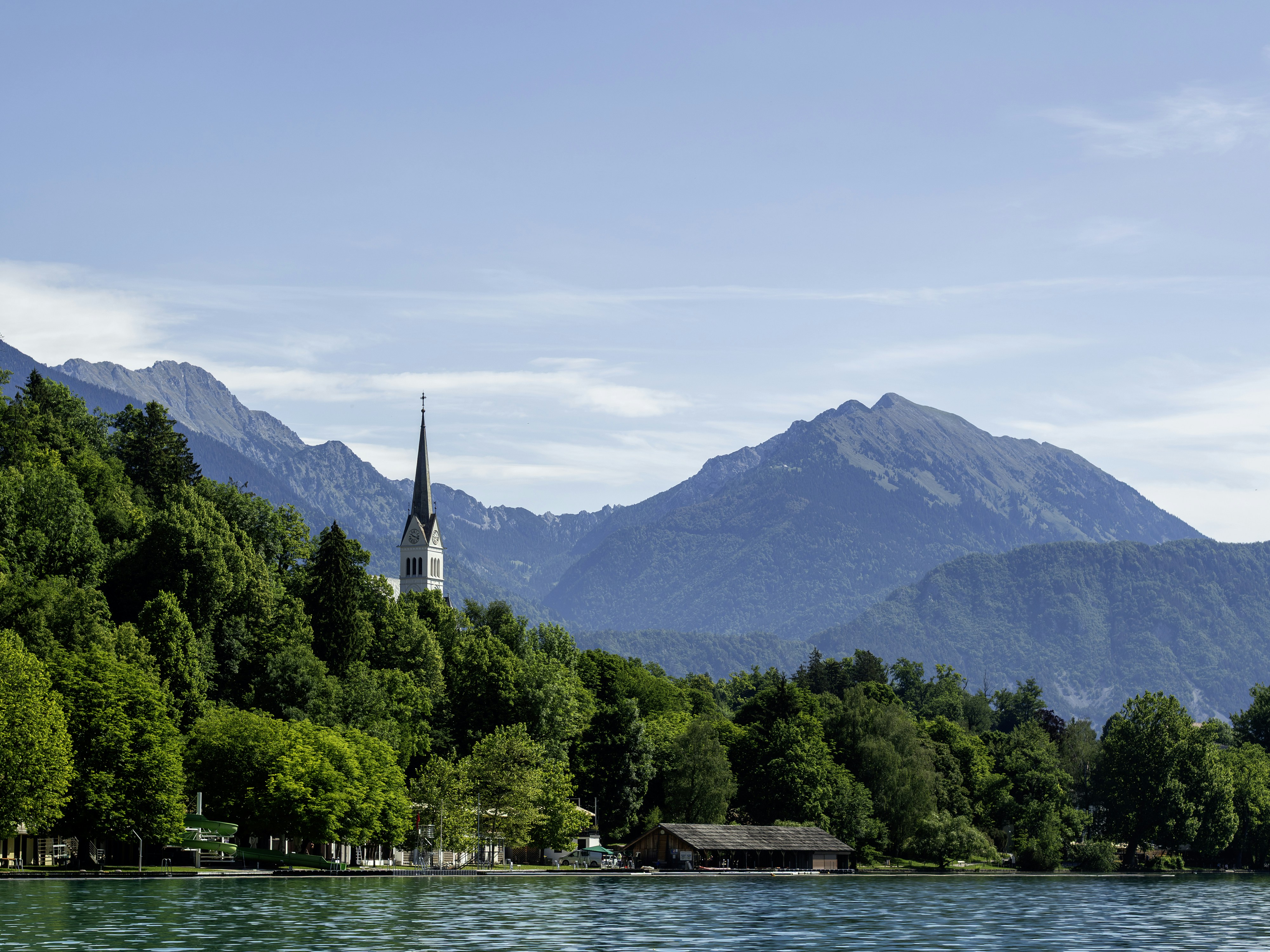 Church Spire Rising Above the Green Shoreline Against Alpine Backdrop