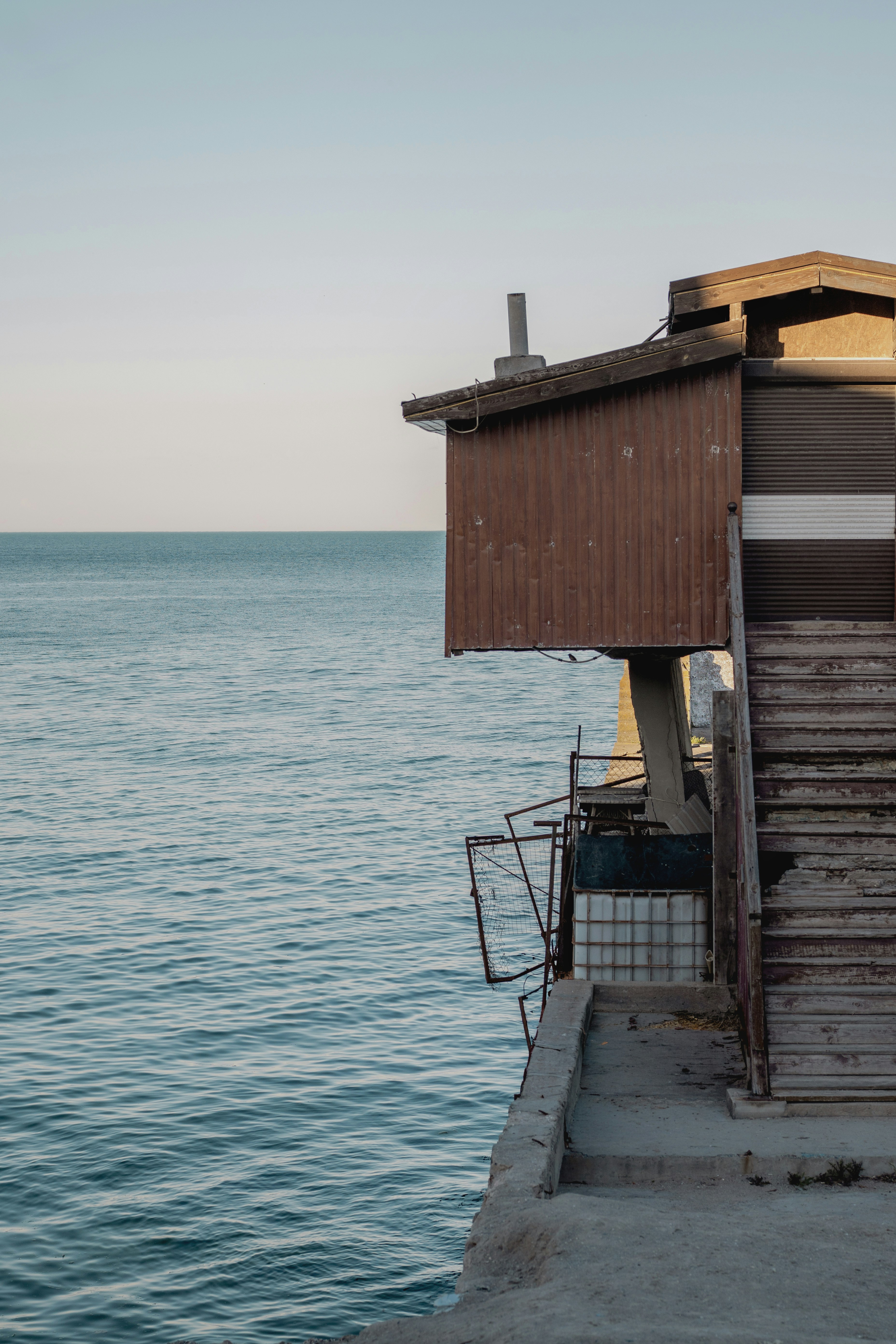 Weathered seaside shack clings to the edge of a concrete jetty