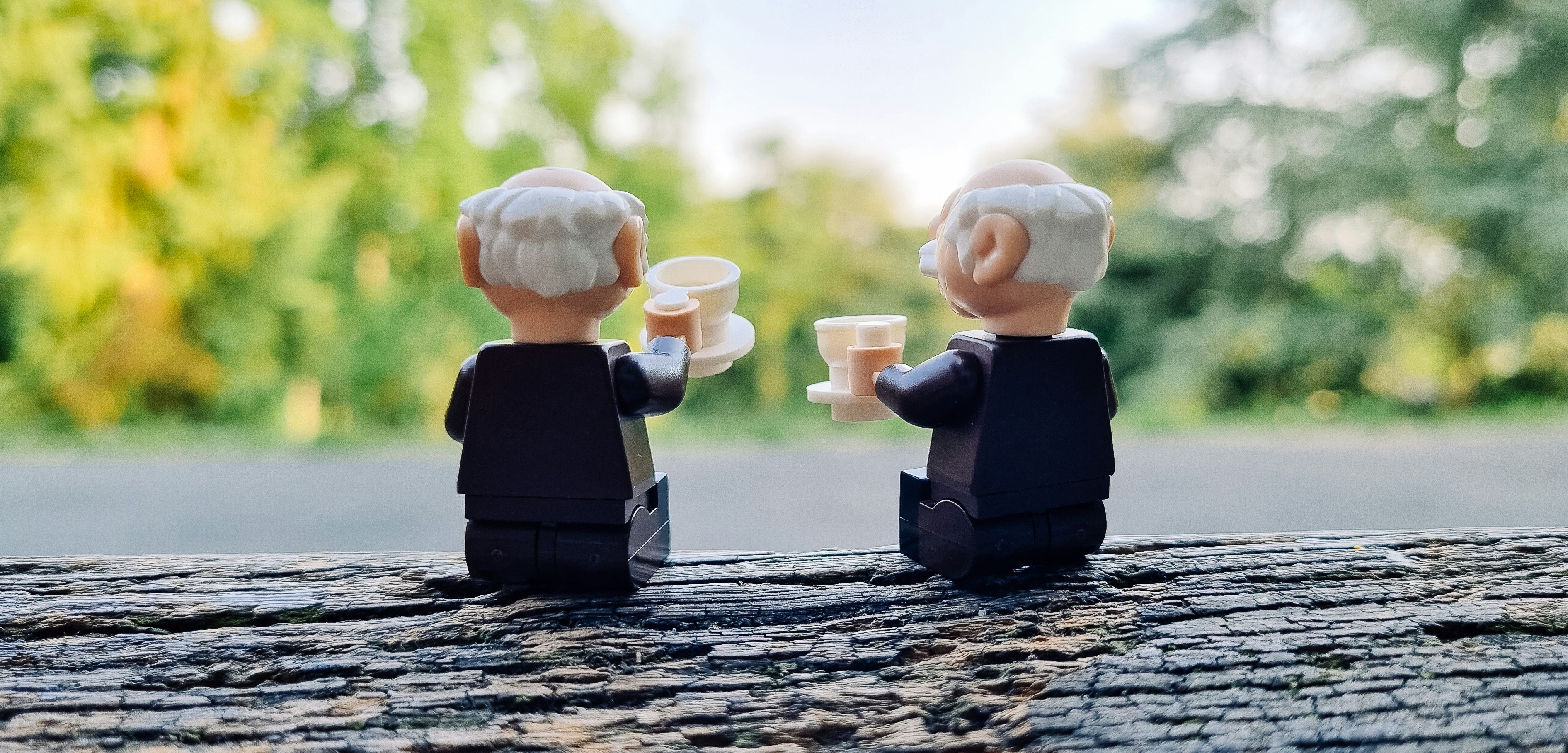 Lego minifigures with grey hair toasting with cups outside.