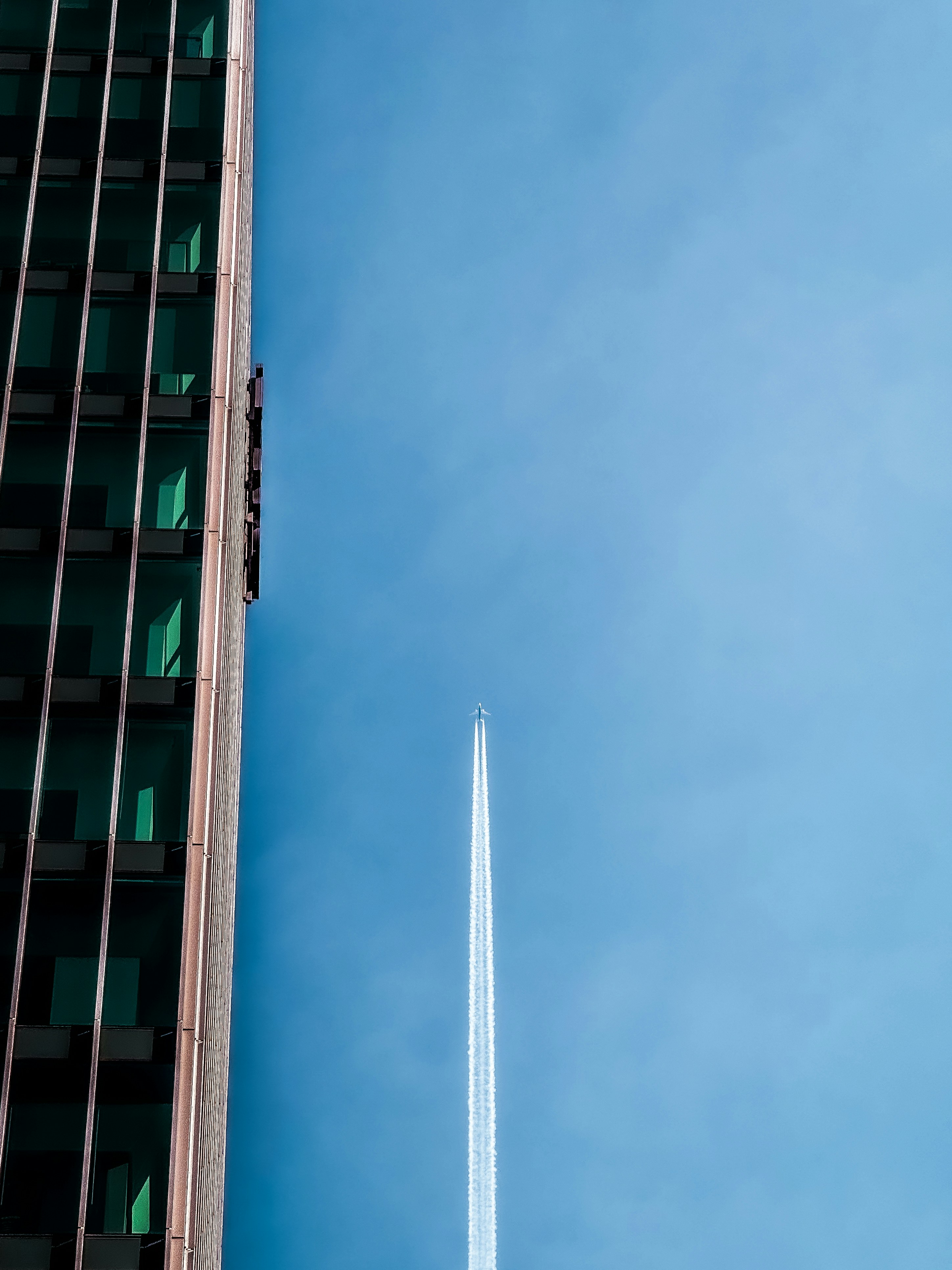 Vertical Trail: Jet of Cloud Cracks the Sky beside a Facade