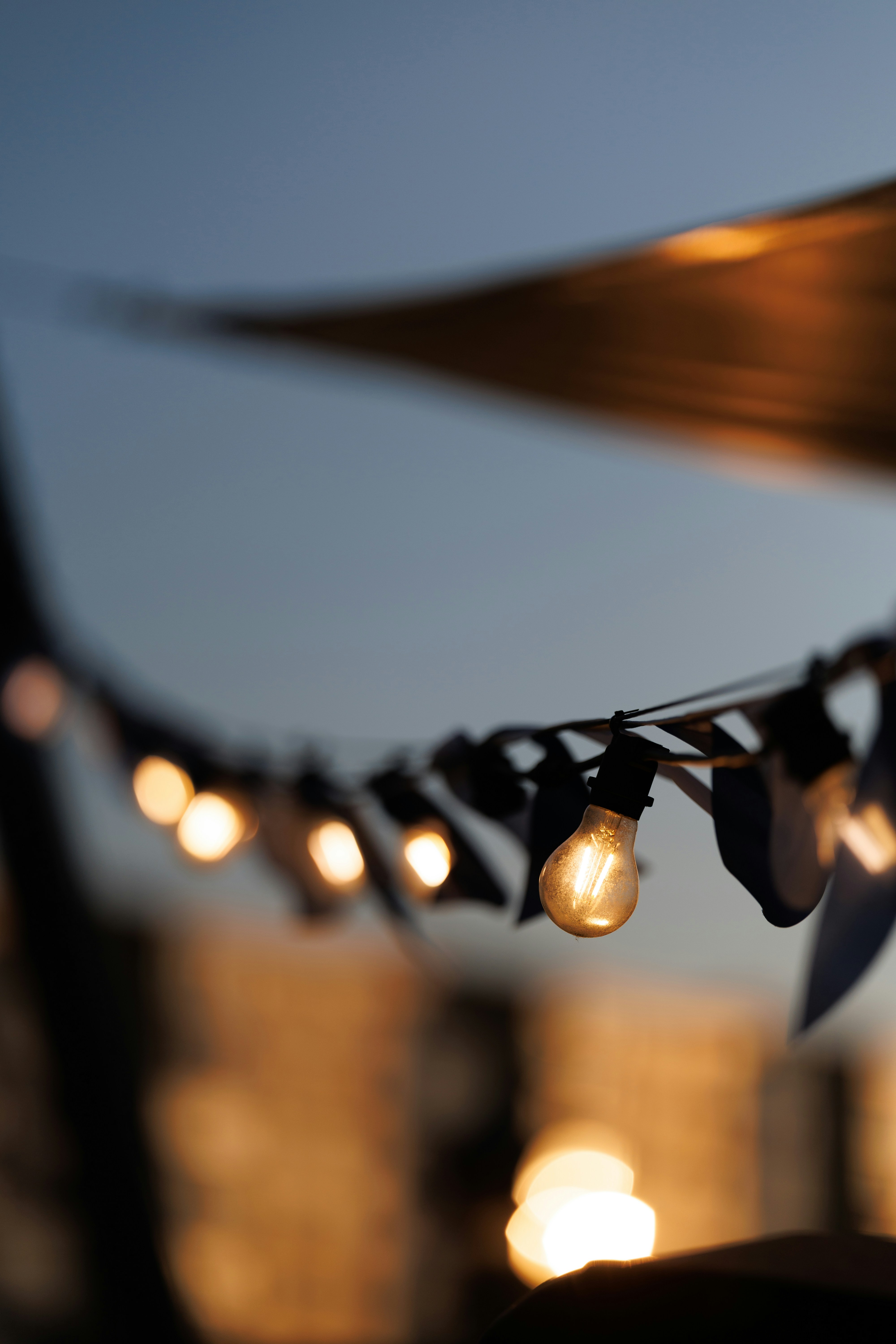 Glowing Bulb Amid Outdoor String Lights at Dusk