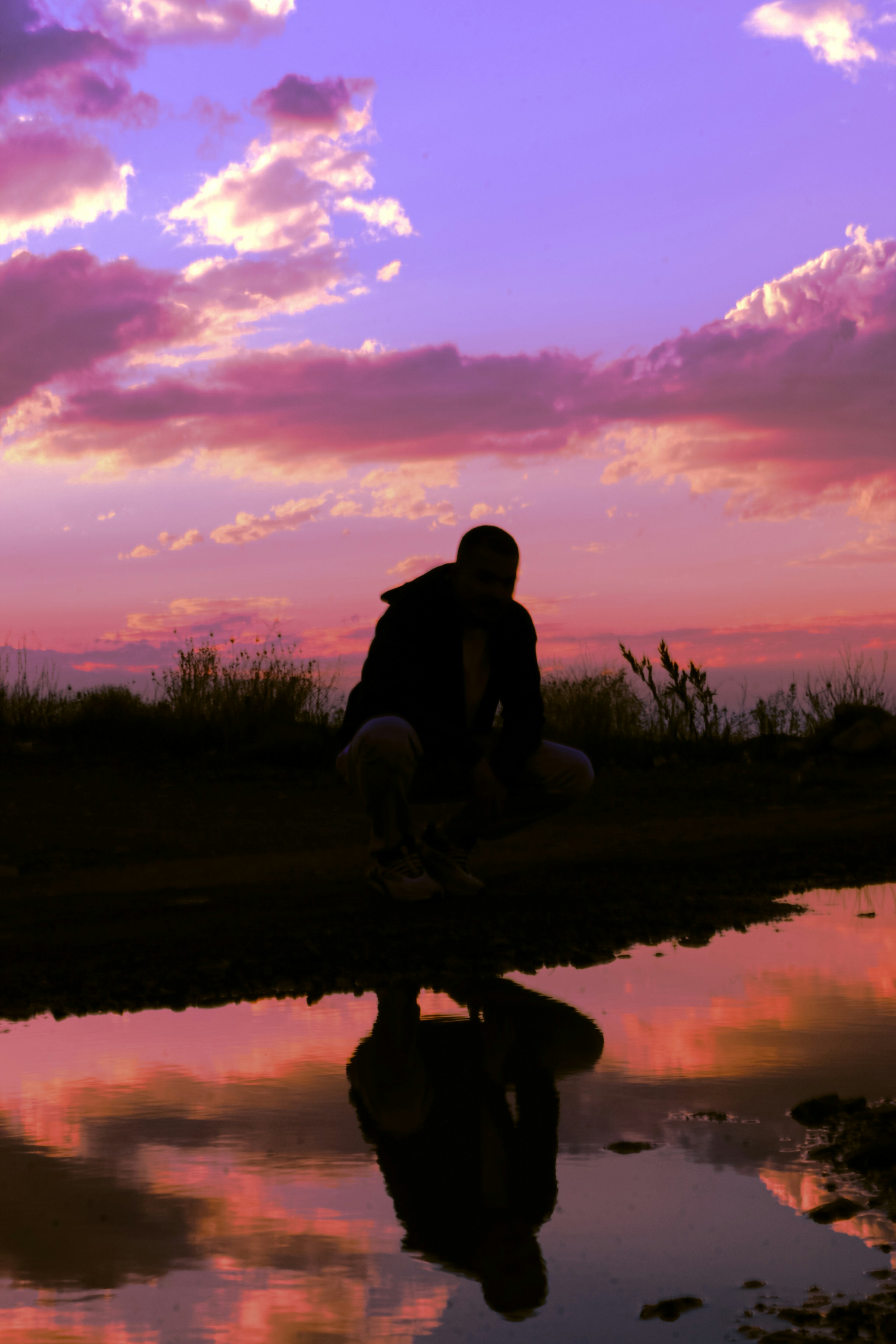 Horizon Silhouette: A Crouched Figure at Sunset by a Reflective Pool