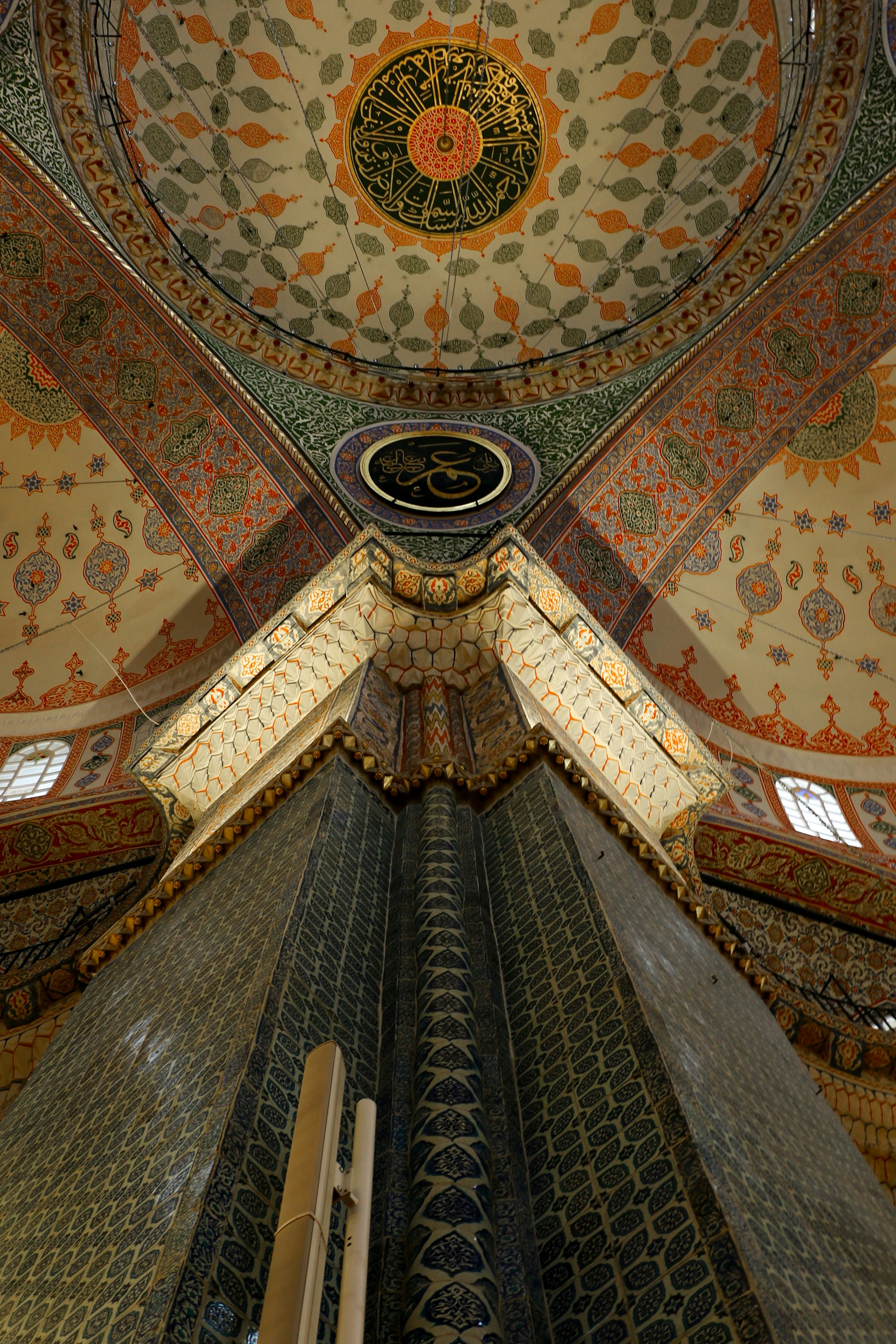 Ceiling vaults and central column converge in a mosque's ornate architectural hall