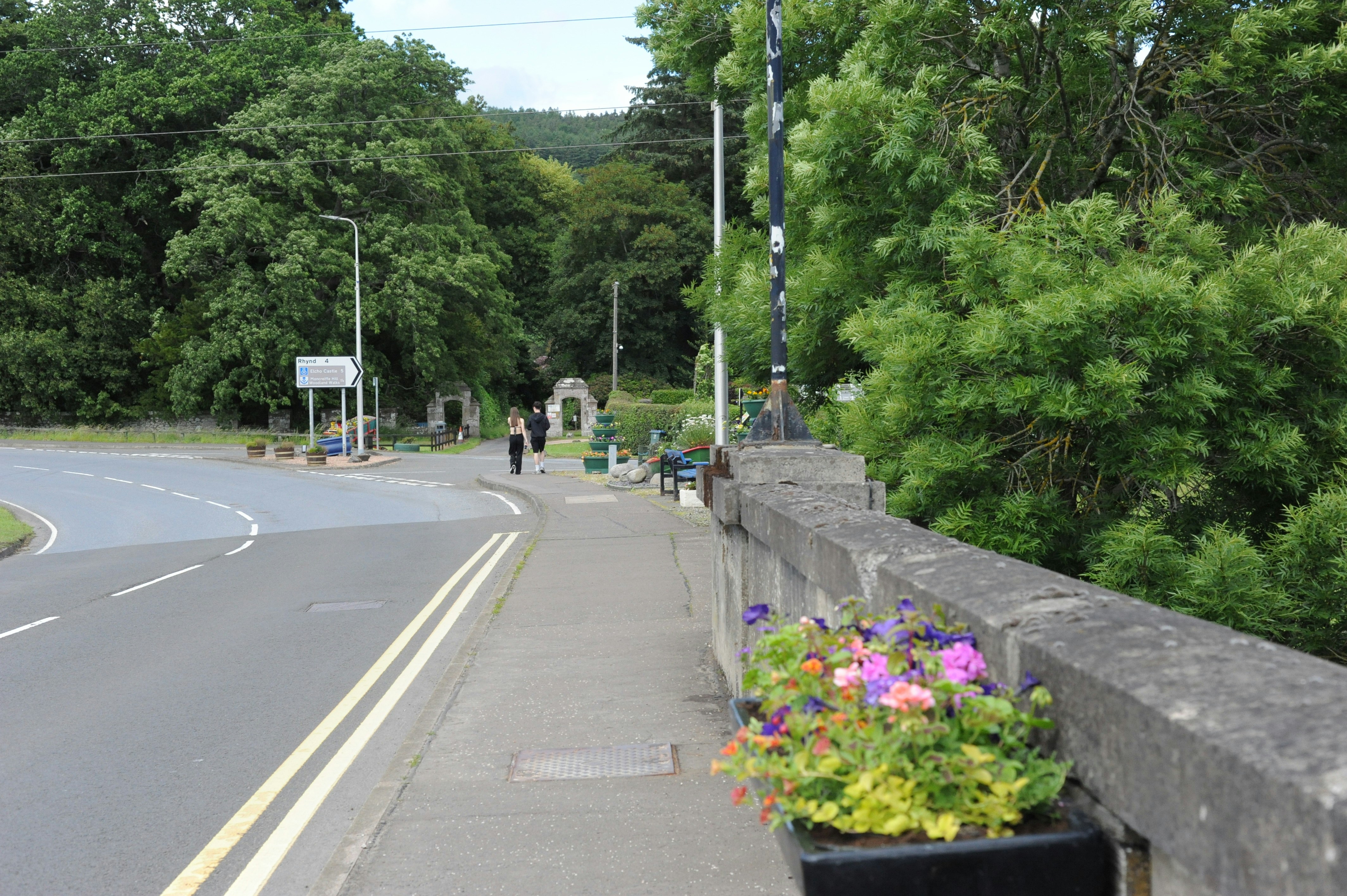 Quiet curving road and flower-filled ledge toward a pedestrian-filled horizon
