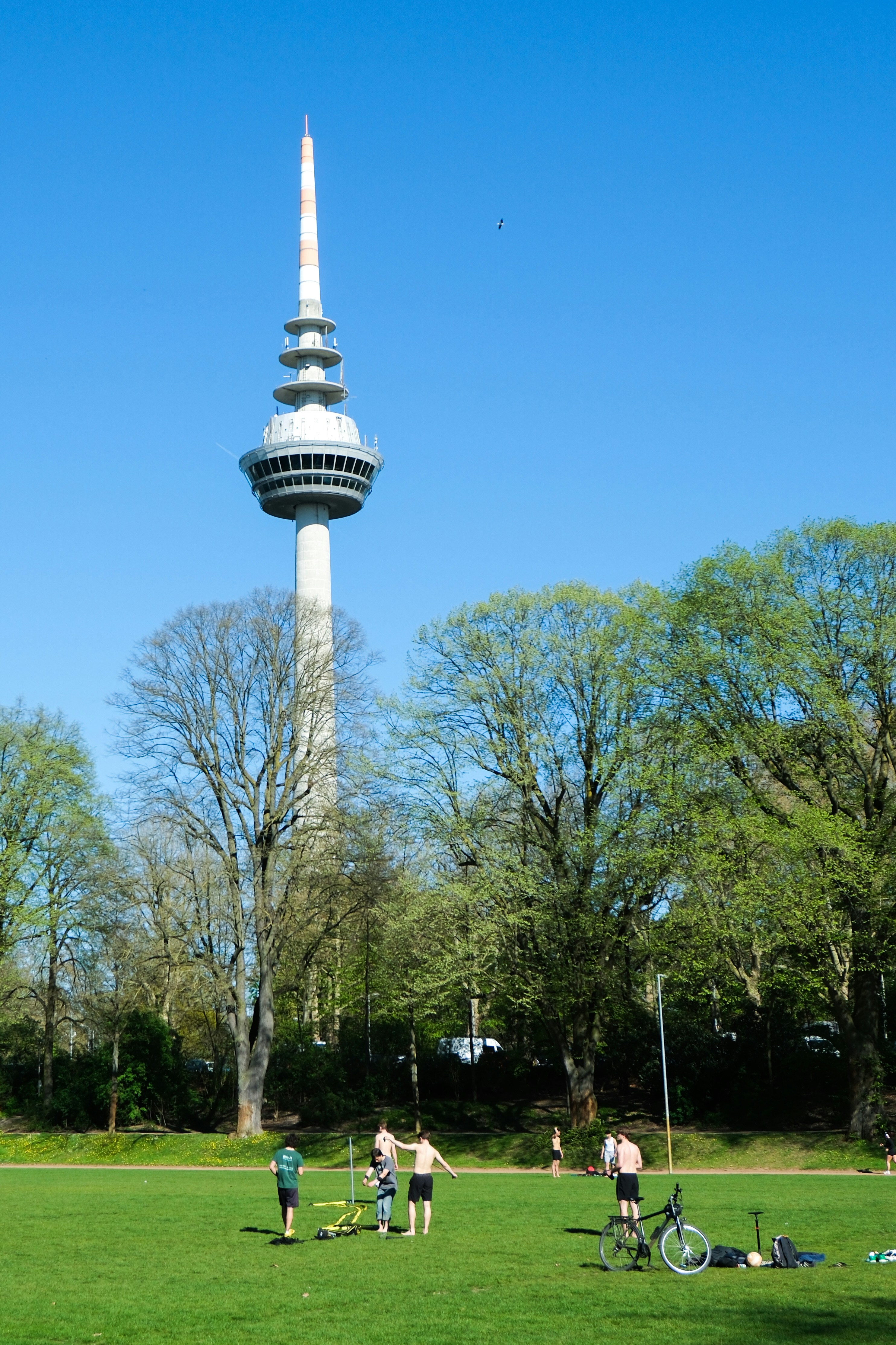 Towering Spire Above the Park: A Sunny Day Scene with People and Bike by the Trees