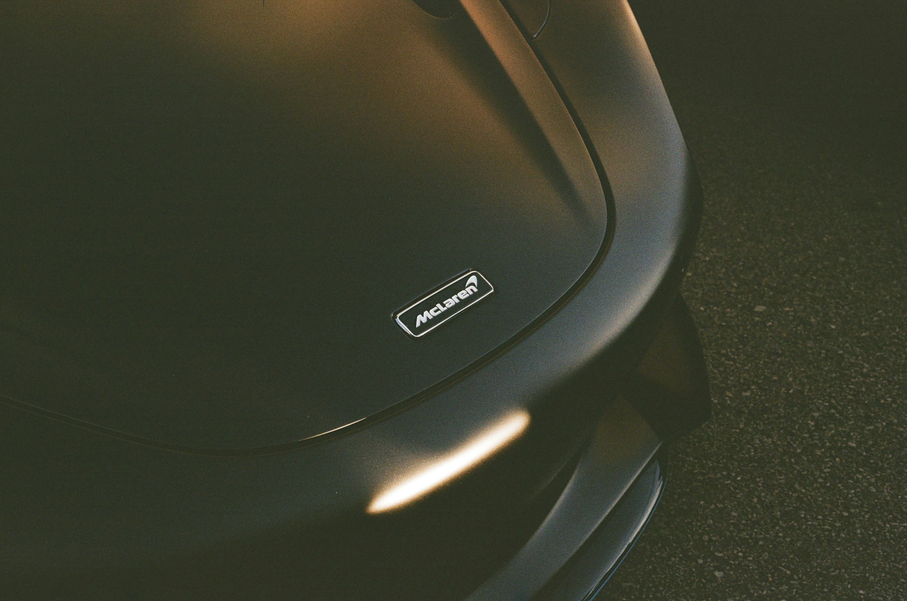 Low-angle close on a matte McLaren badge and hood line