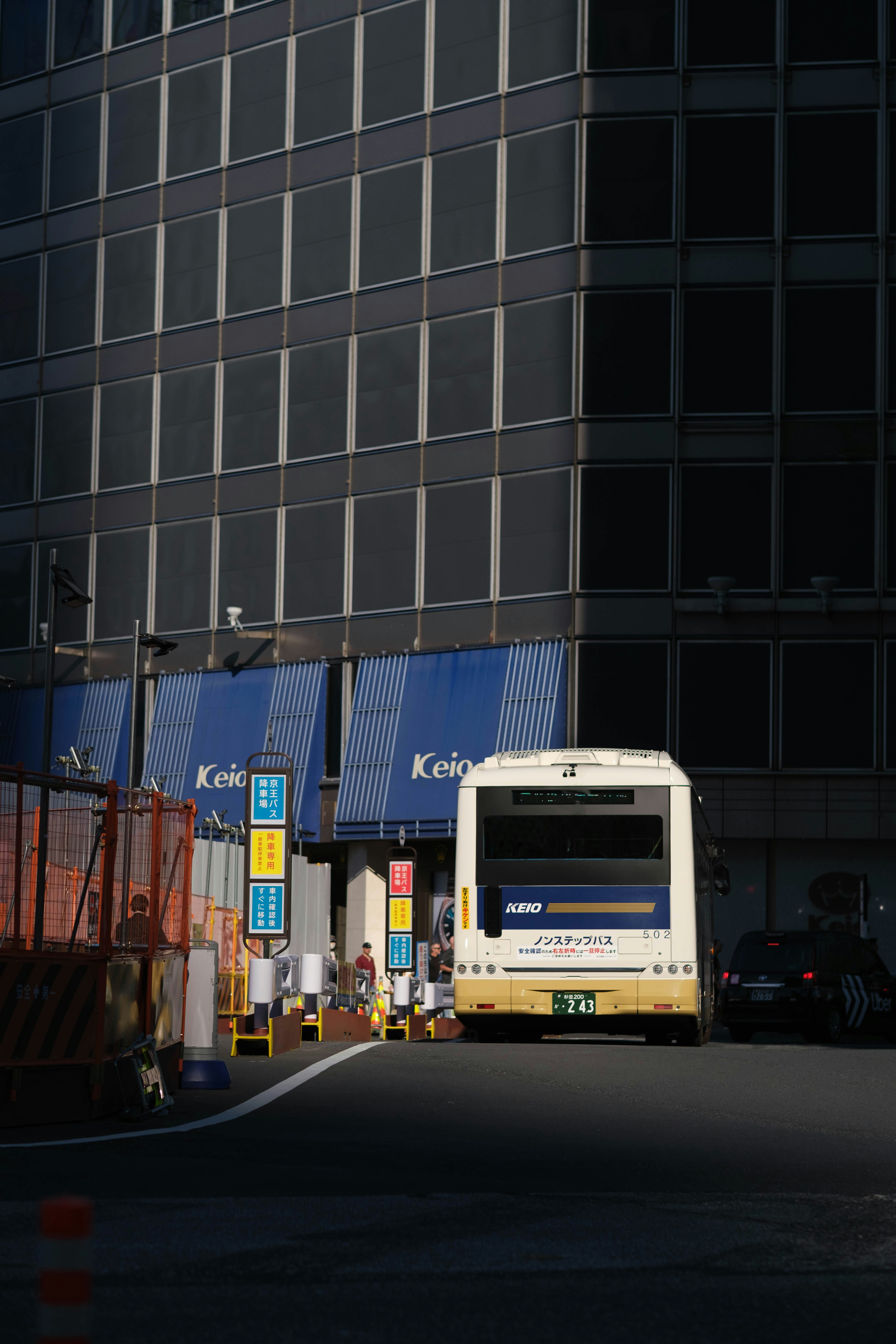 Bus on a city street lined with blue storefronts and construction barriers beside a glass-front building.
