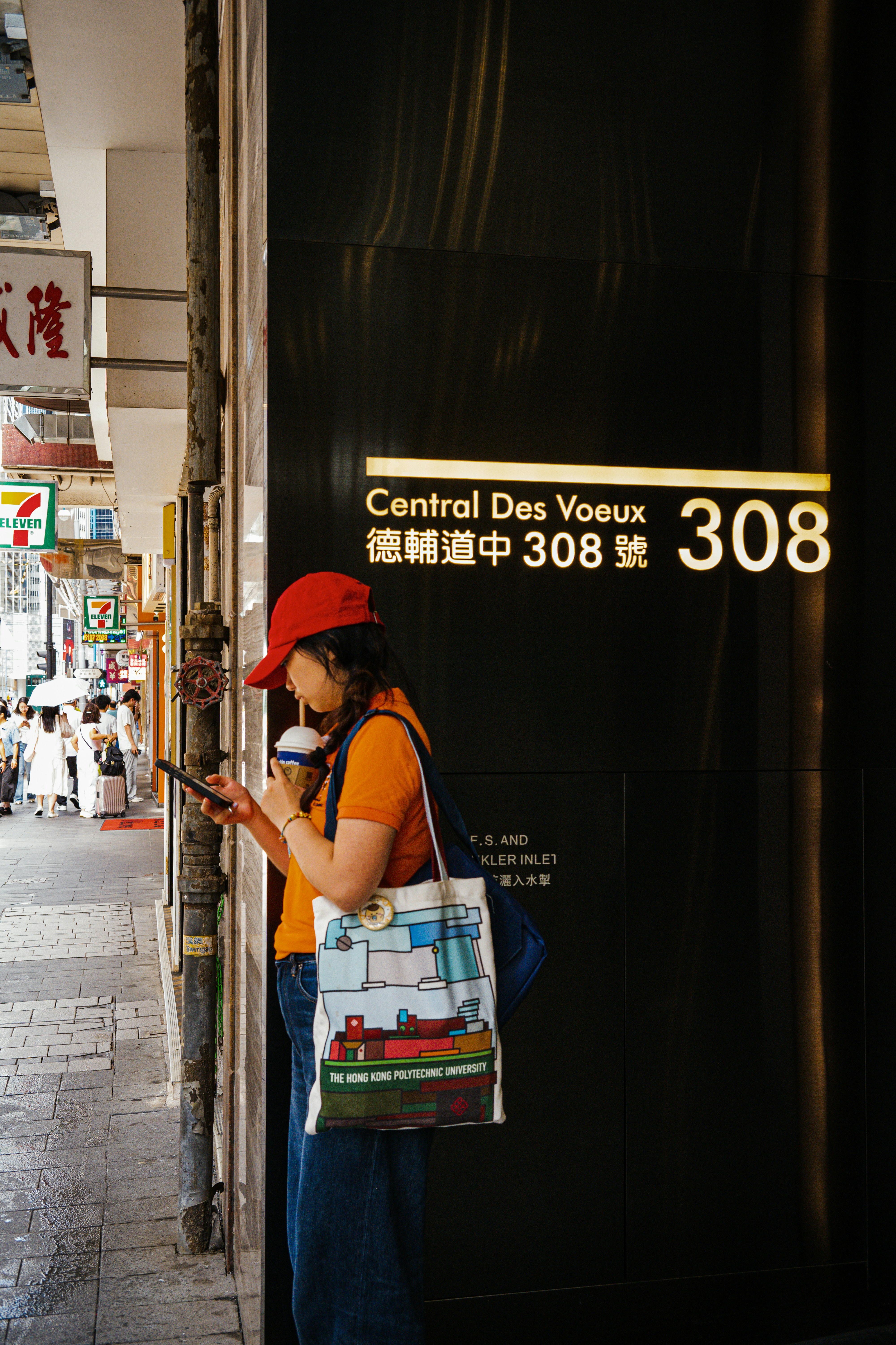 Orange Hoodie, Red Cap, and City Street: A Traveler Glances at Her Screen