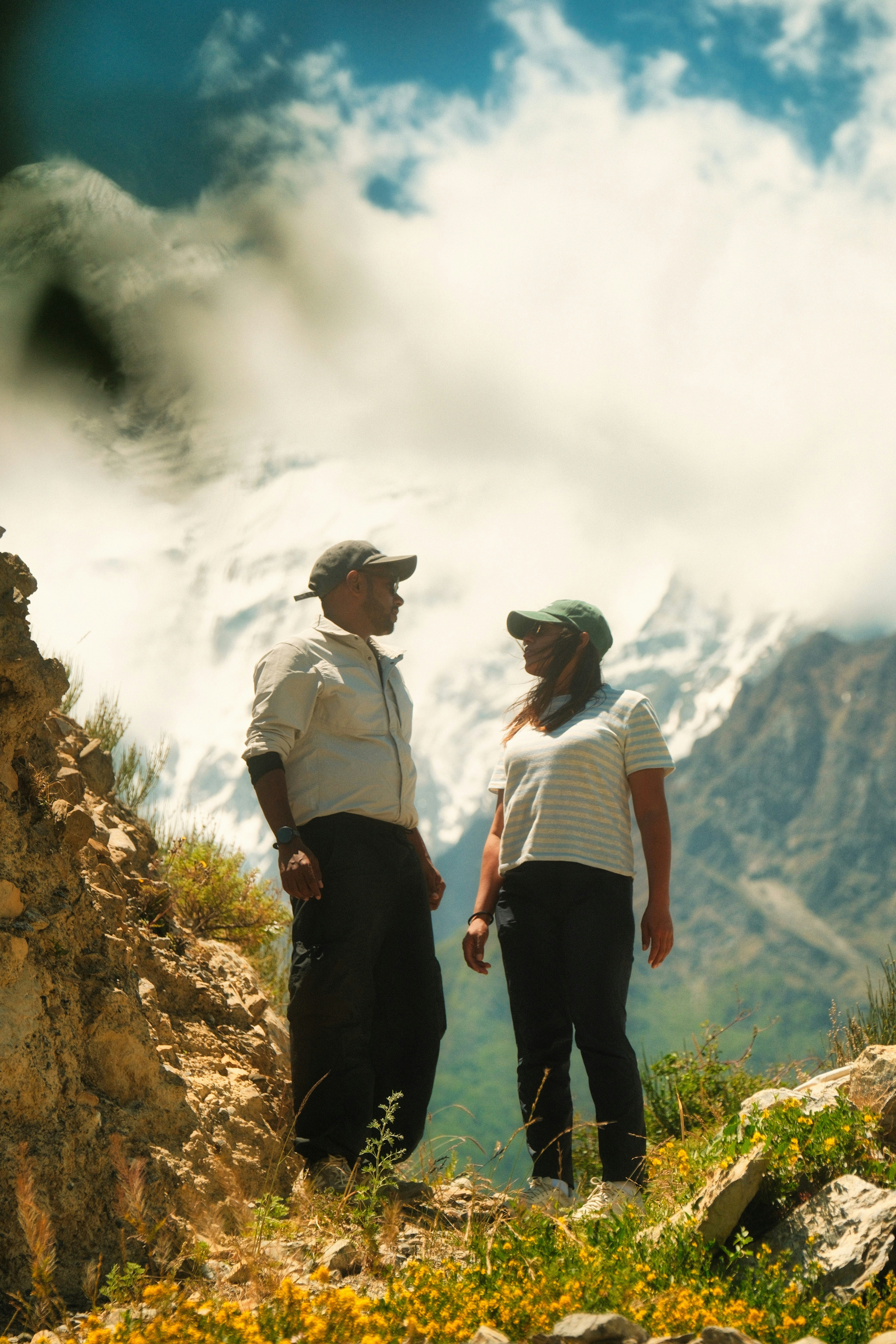 Two Explorers Stand Tall Amid Mountain Veil and Wildflowers